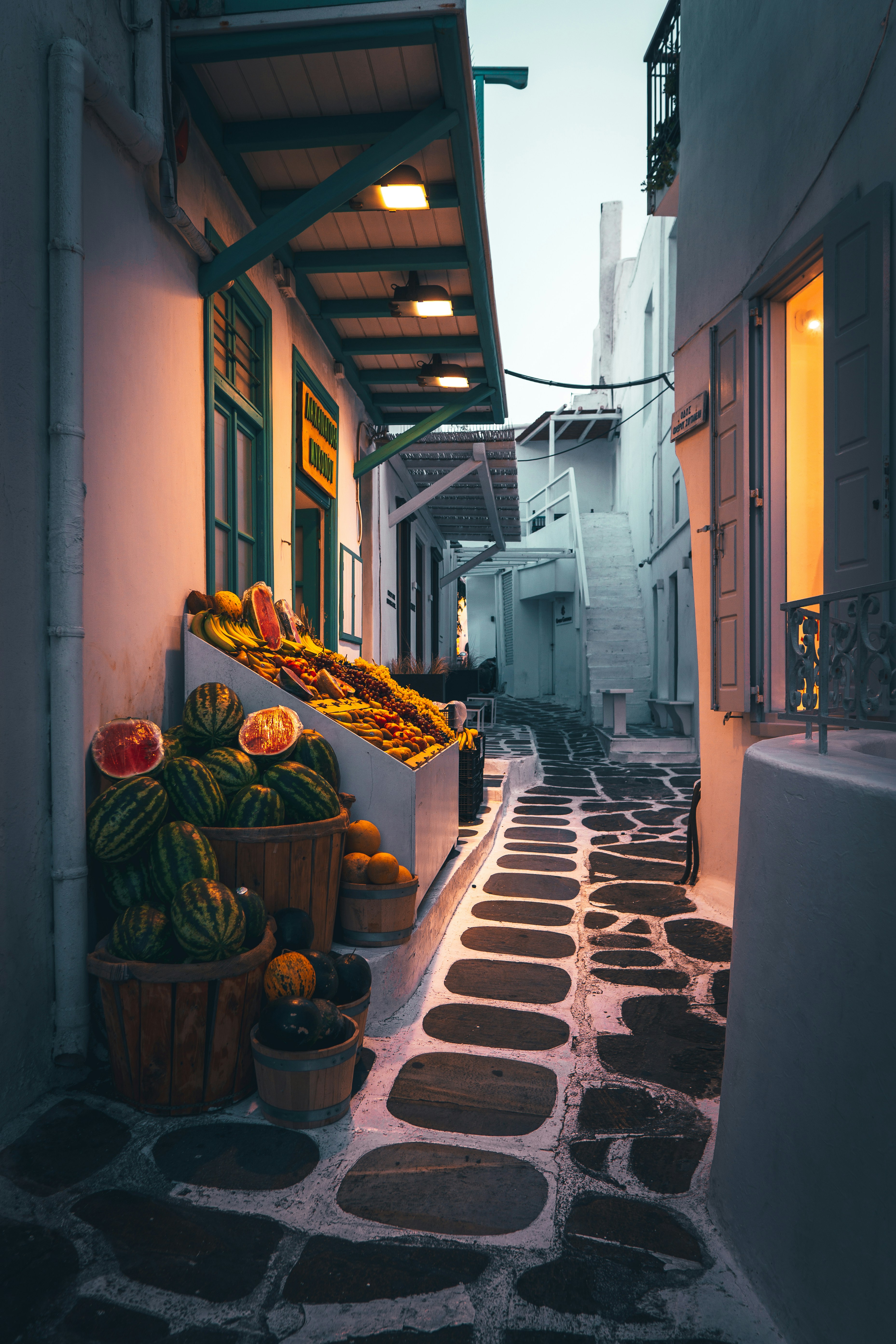 Vibrant display of fresh fruits in wooden baskets lining a narrow cobblestone alley at twilight, leading into a softly lit passageway.