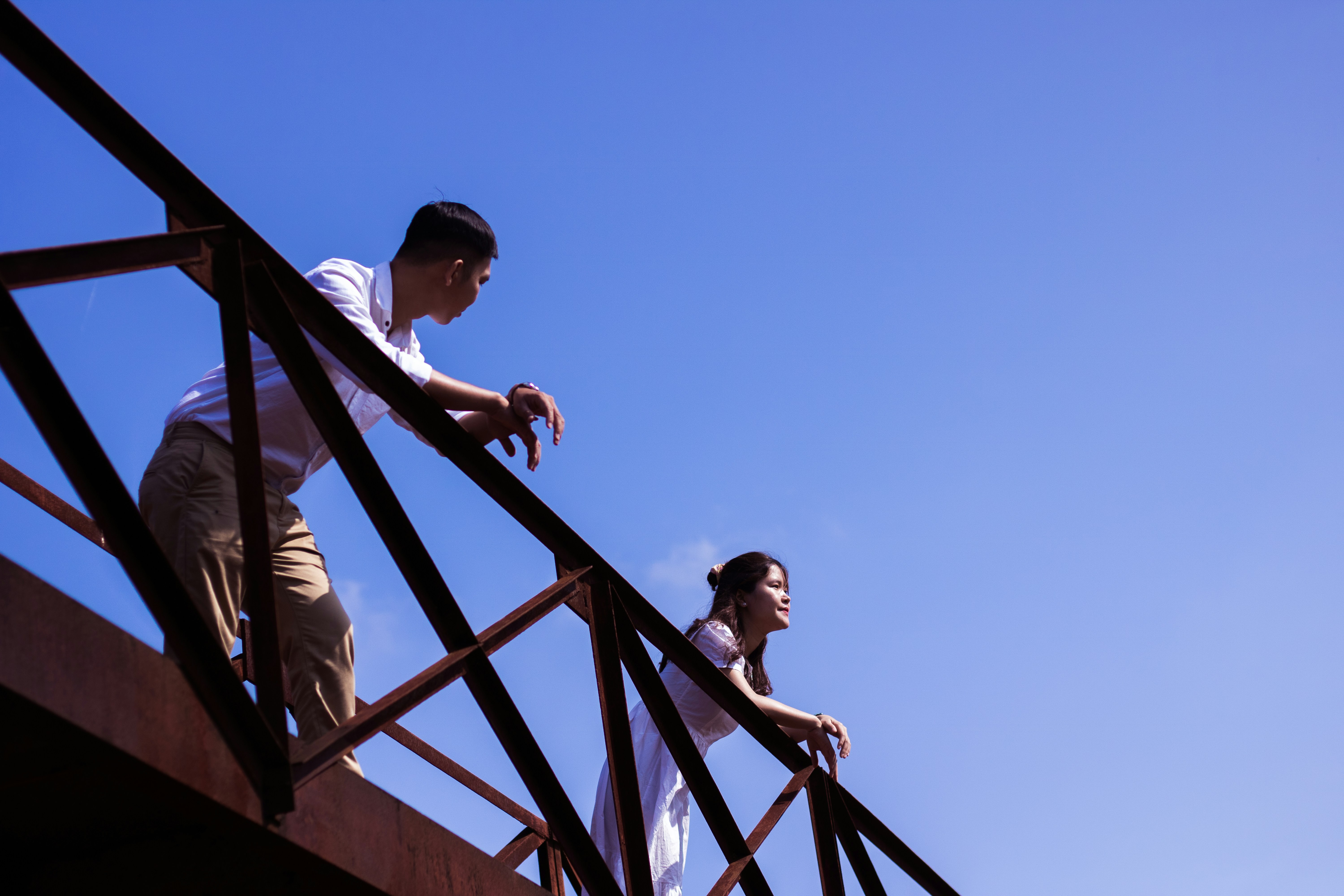 Edge of the Frame: Two Figures on a Rusted Bridge Against a Cerulean Sky