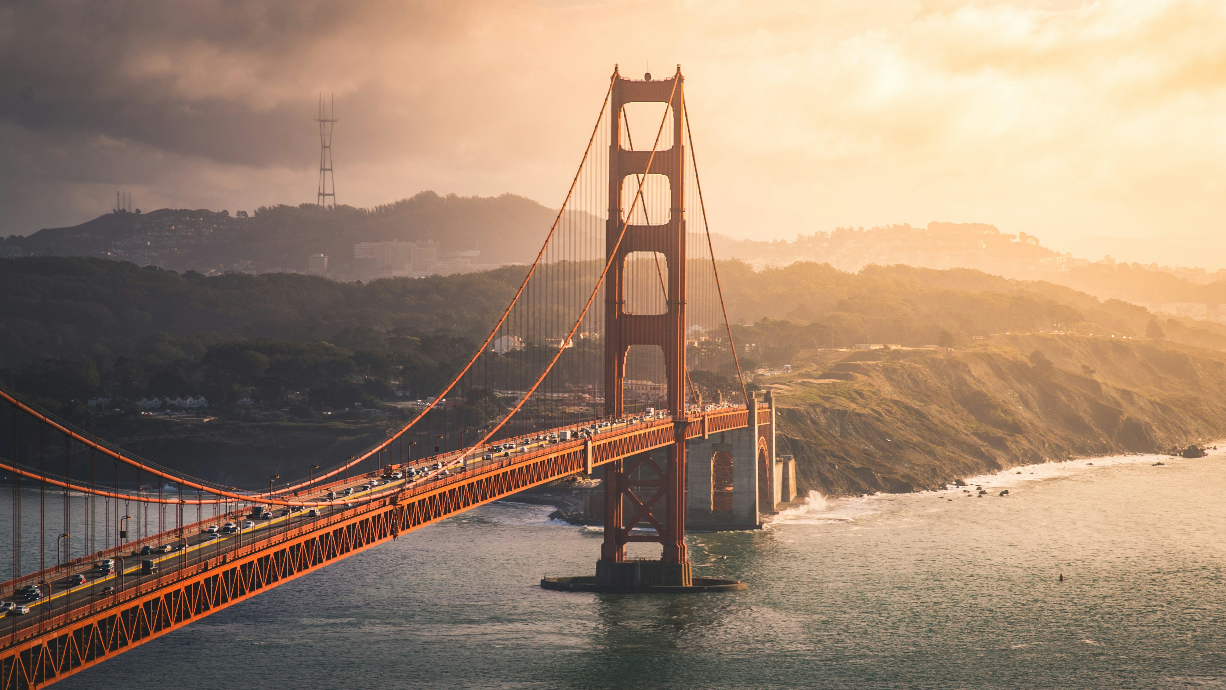 Golden Gate Bridge extending over misty bay under dramatic, golden-hued sky.