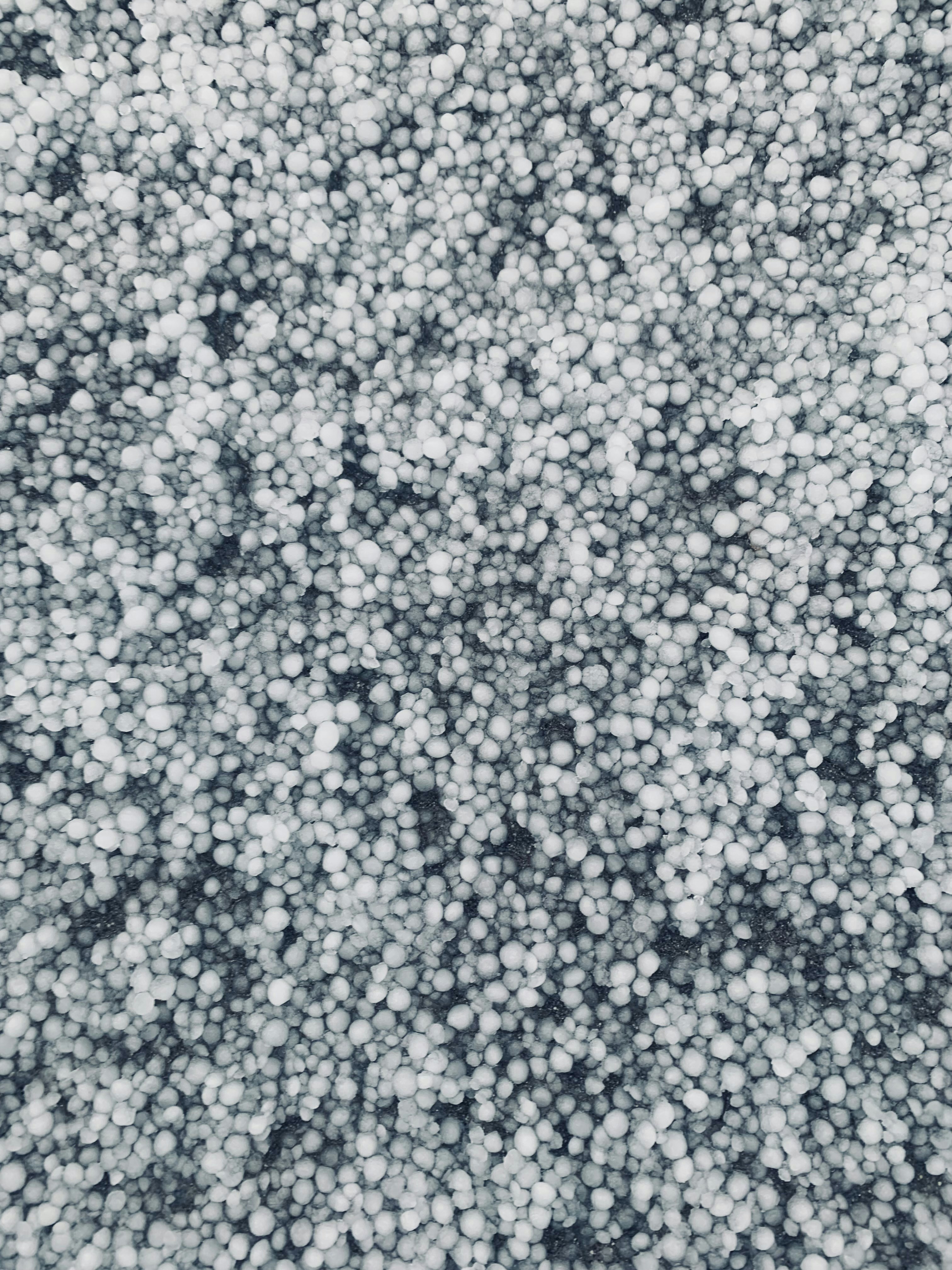 Close-up view of a textured surface covered in tiny white beads resembling snow or frost. The intricate pattern creates an abstract visual effect.