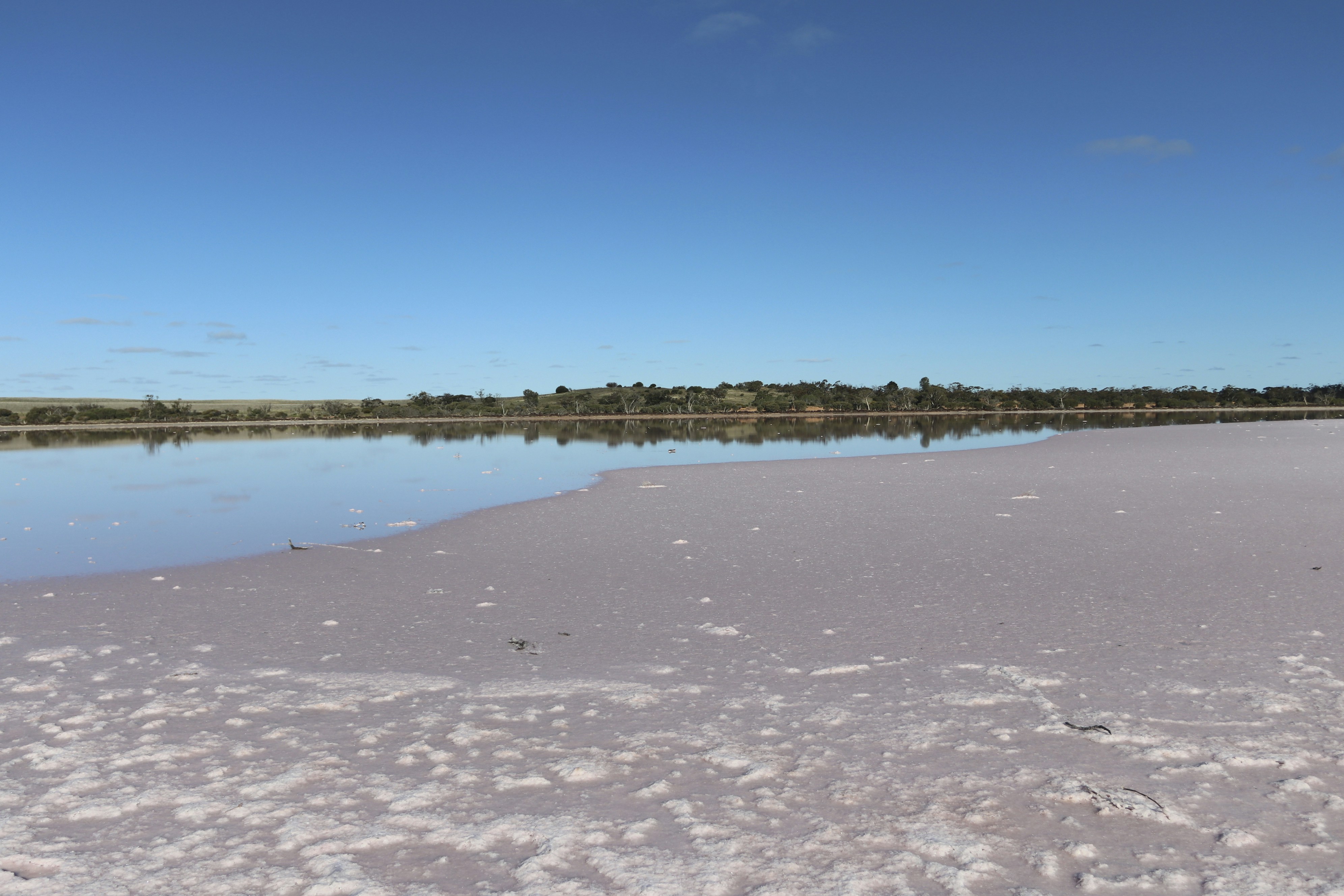 Expansive salt flat leading to a calm, reflective lake under a clear blue sky.
