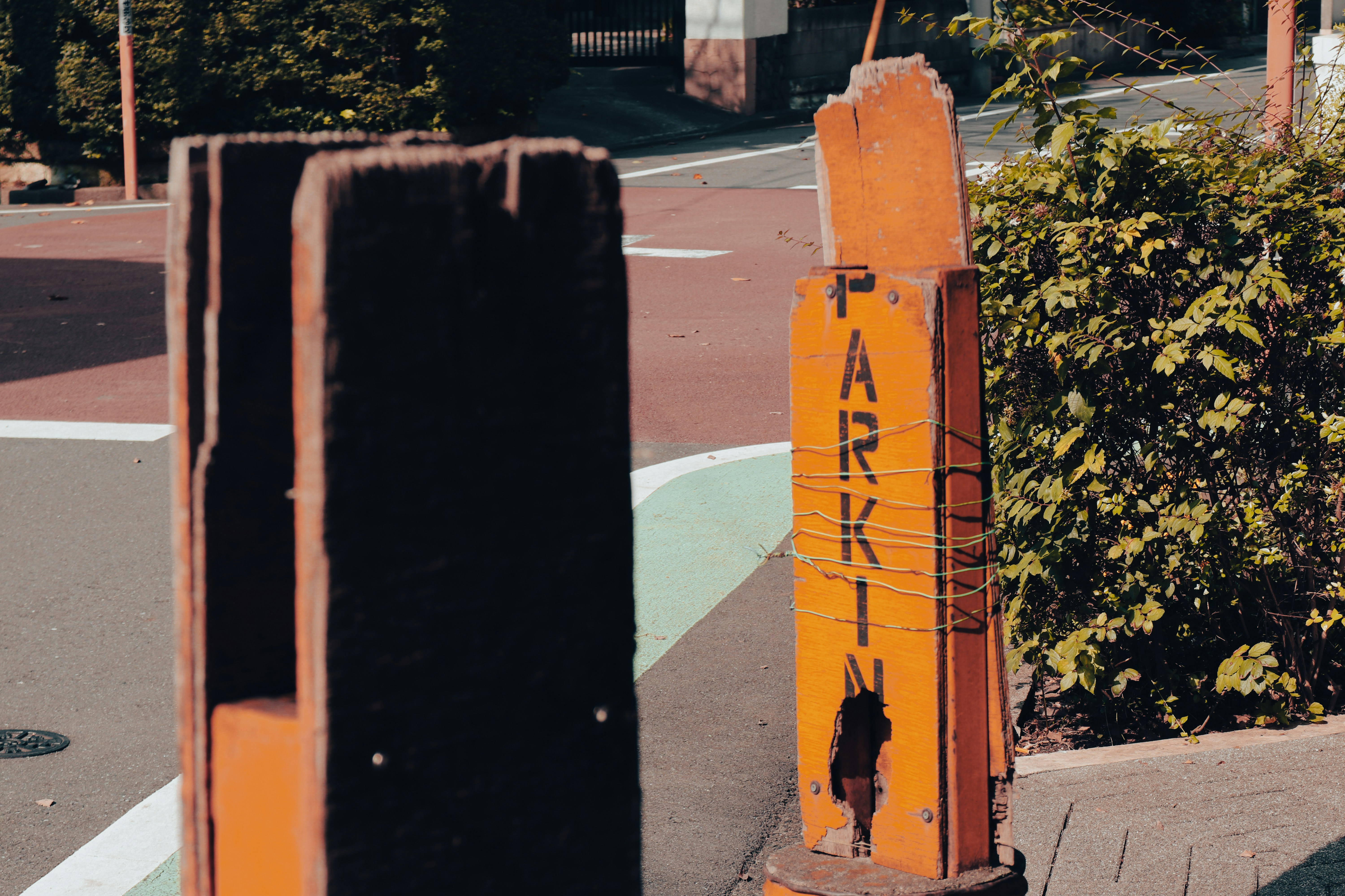 Weathered parking posts stand against a backdrop of urban greenery, hinting at a forgotten space. The vibrant orange contrasts with the muted surroundings.