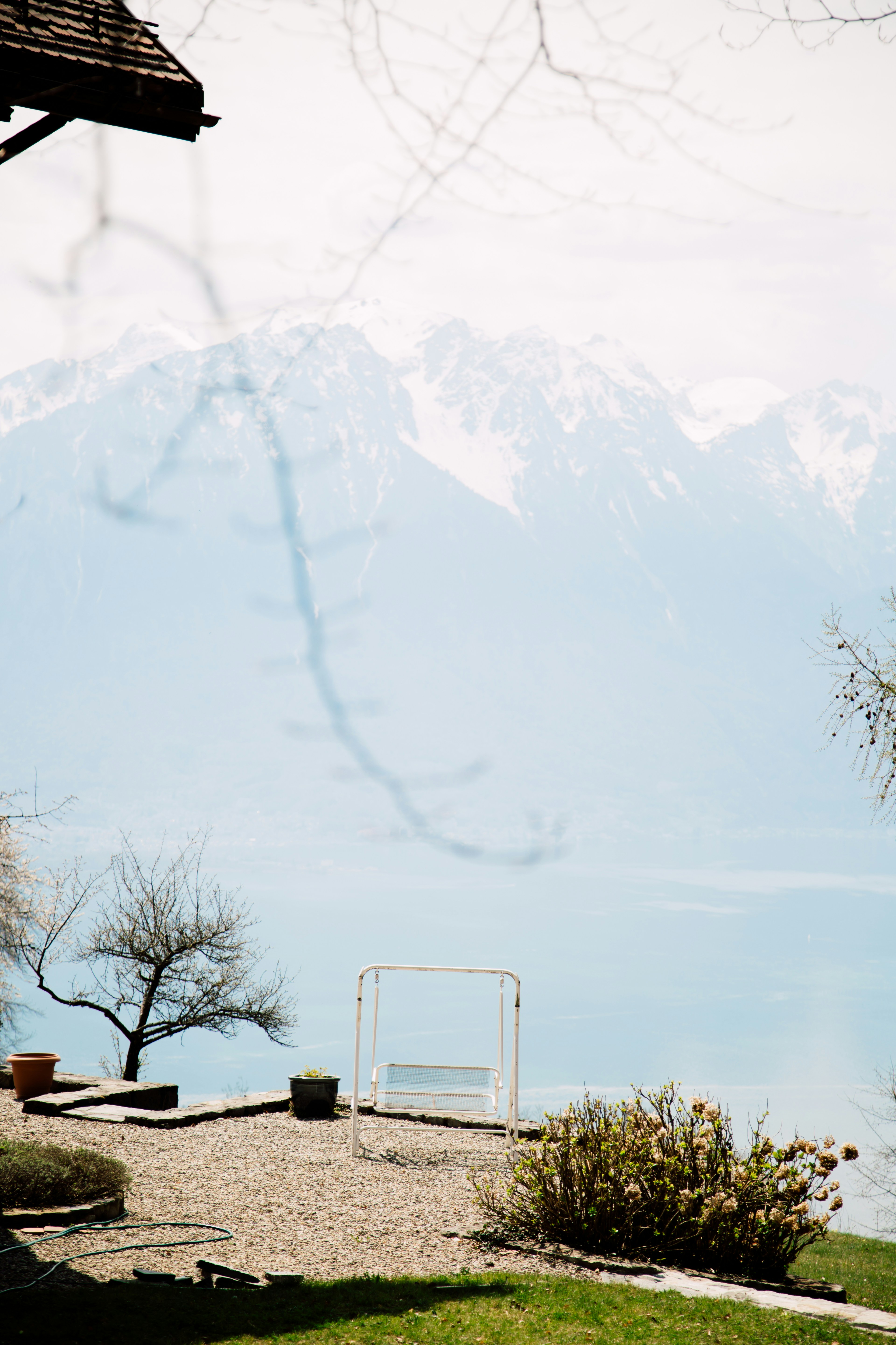 A serene outdoor space featuring a swing set and lush greenery, framed by distant snow-capped mountains and a tranquil lake.