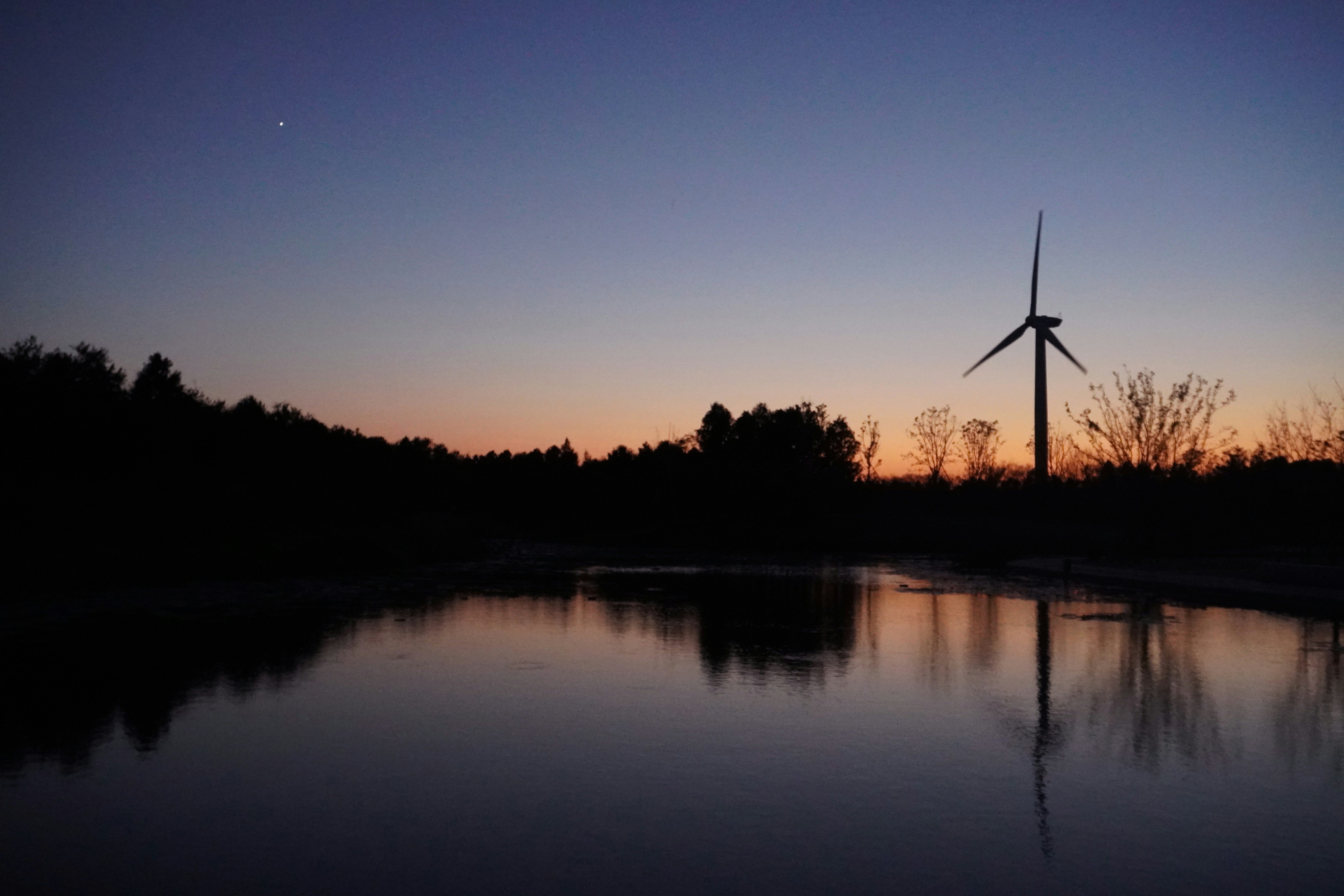 The sun is setting over a lake with a windmill in the background photo ...