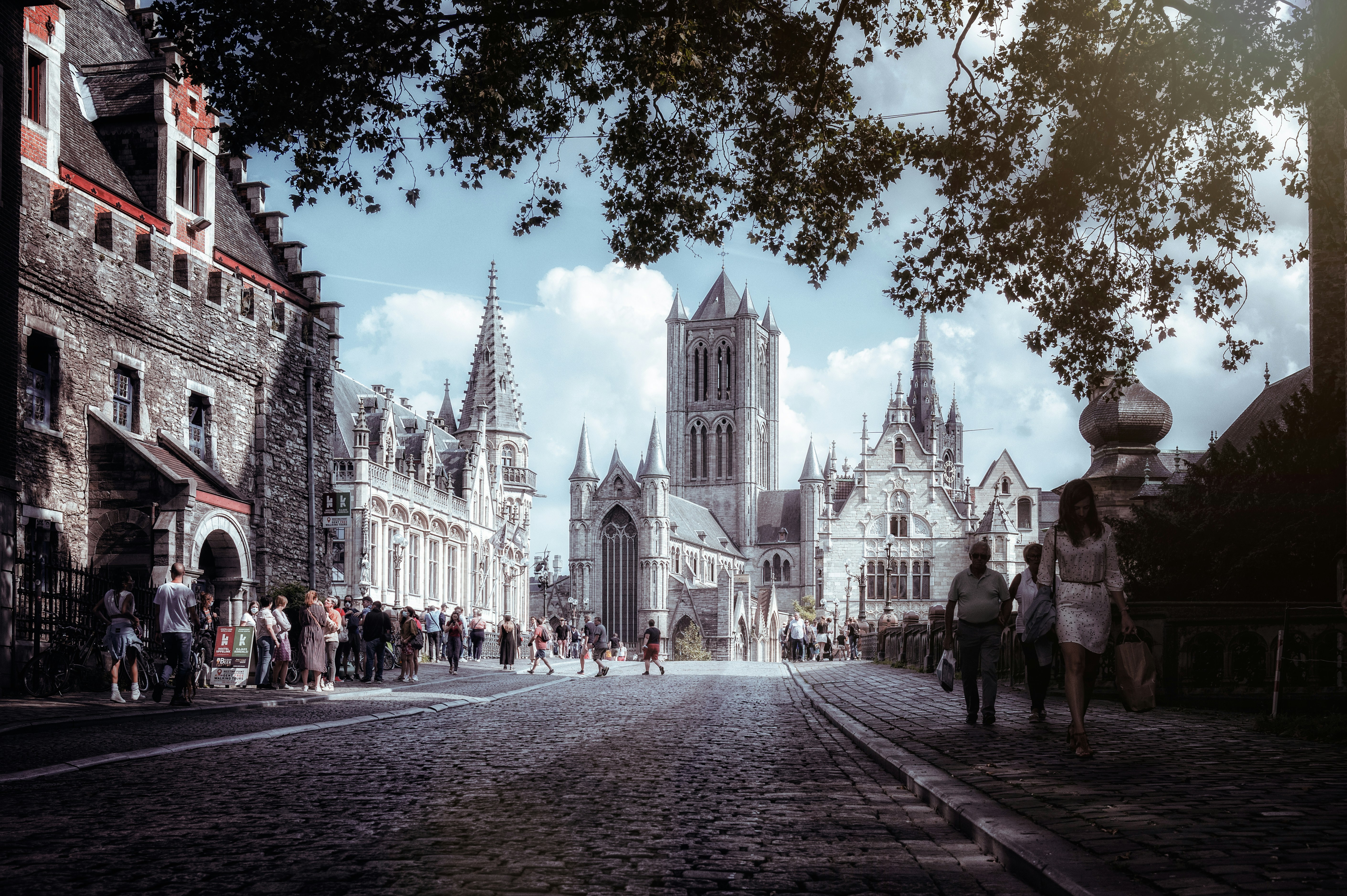 Historic cathedral framed by tree branches with people strolling along the cobblestone street.