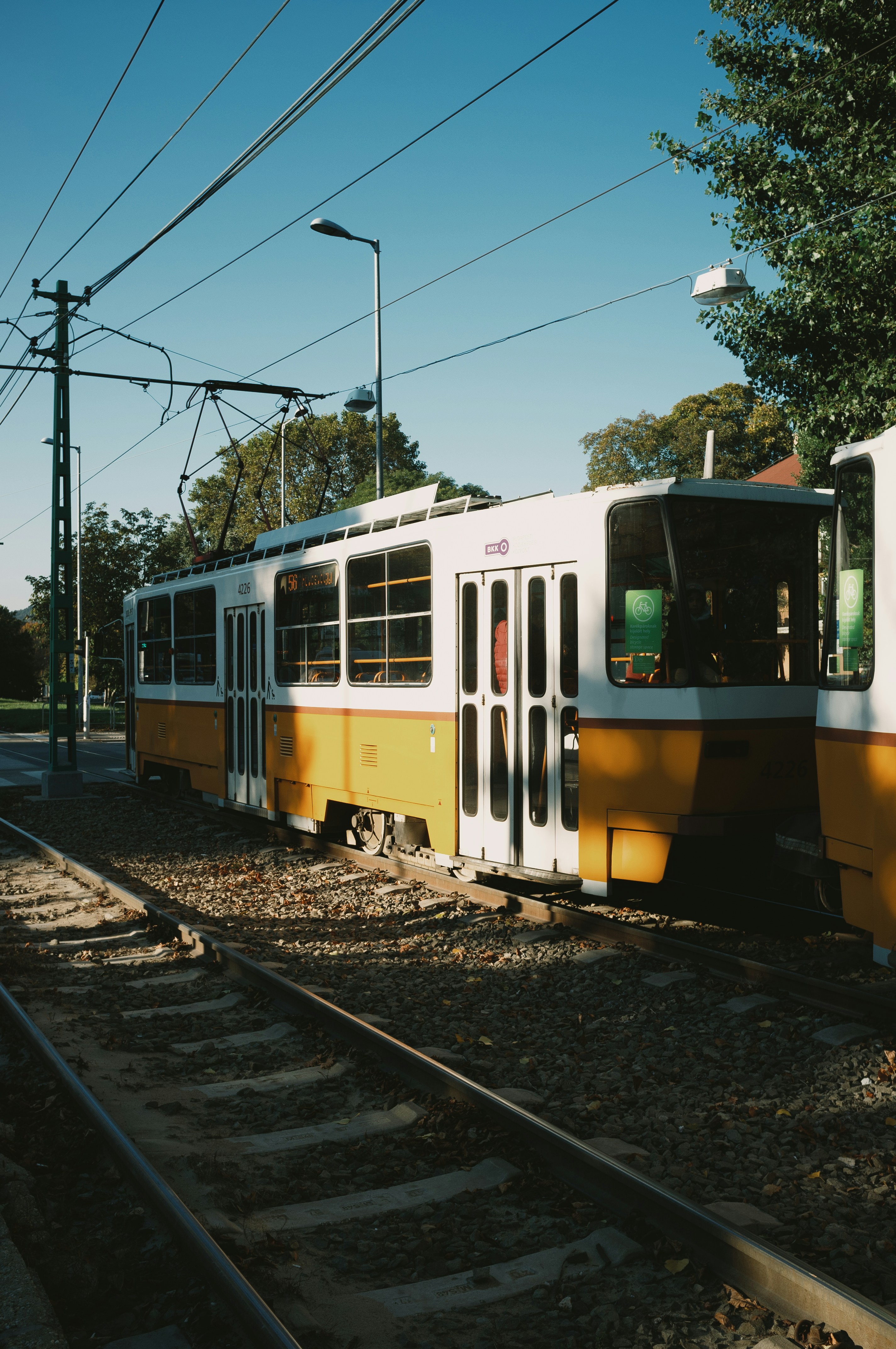 Yellow tram navigating through the city streets, framed by clear blue skies and urban greenery.