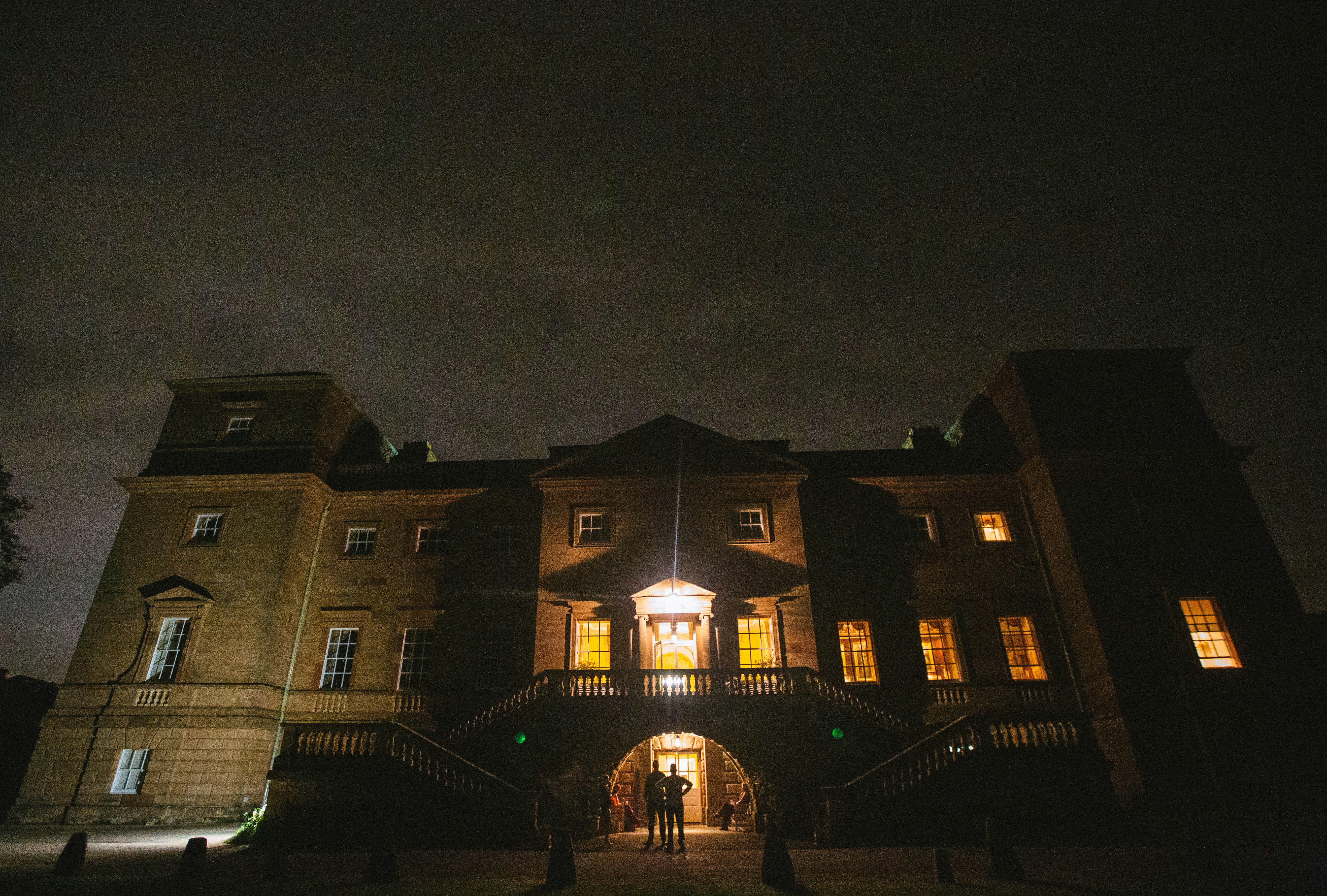 Historic building illuminated at night, showcasing architectural details and inviting entrance. Two figures stand in front, adding a sense of scale.