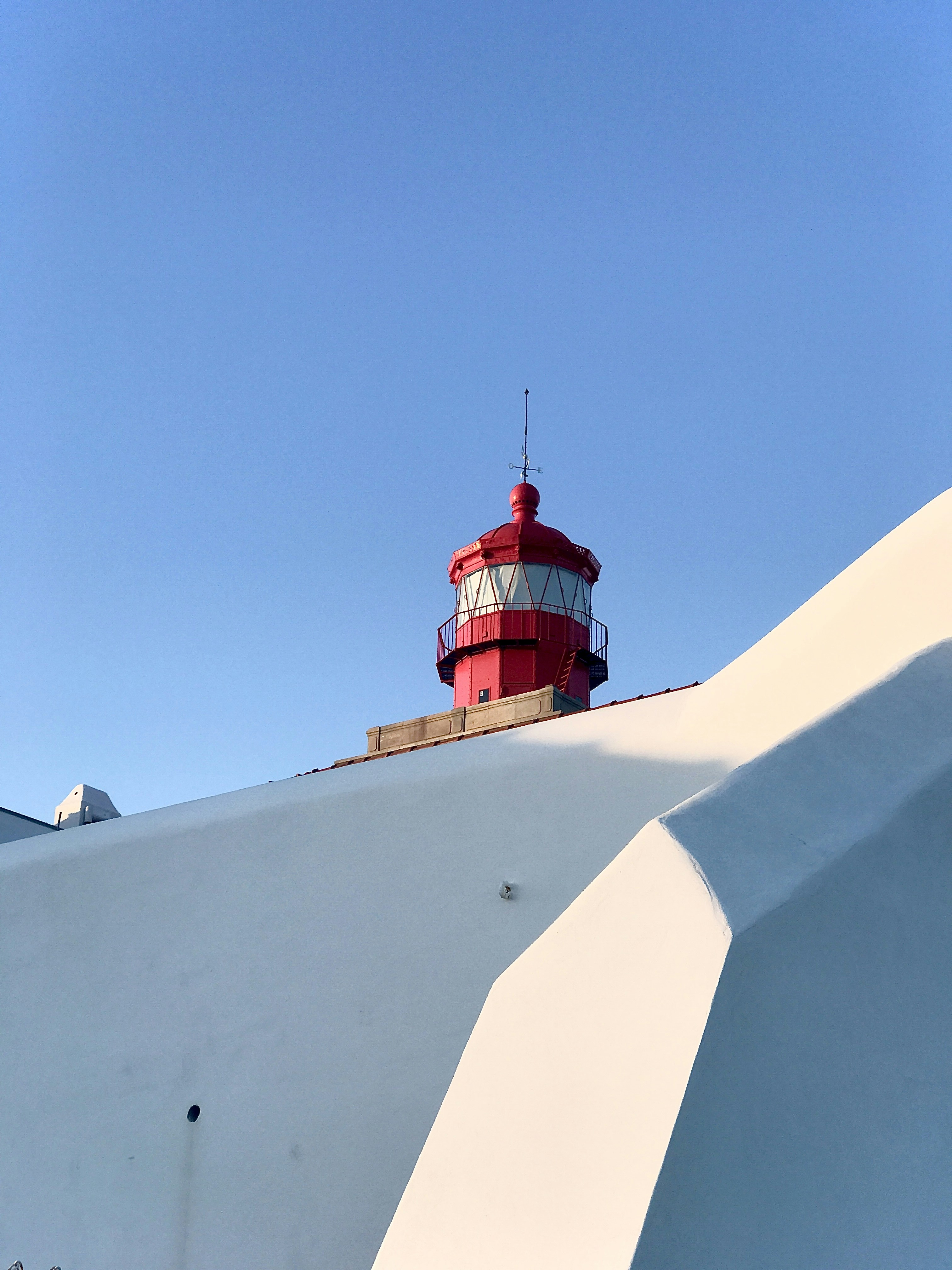 A vibrant red lighthouse stands atop a white structure under a clear blue sky.