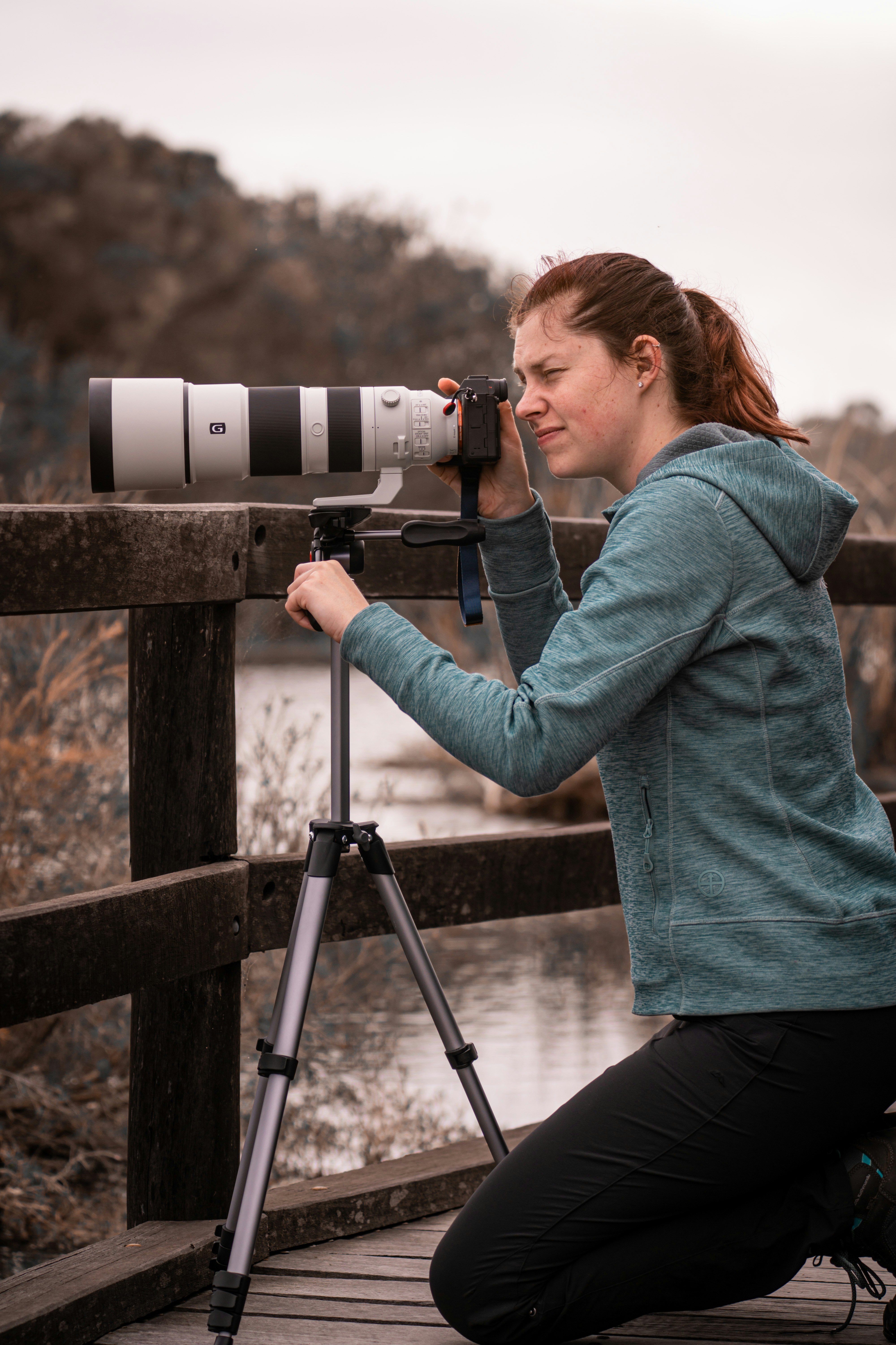 Riverbank Focus: A Photographer Aligns a White Telephoto on a Tripod