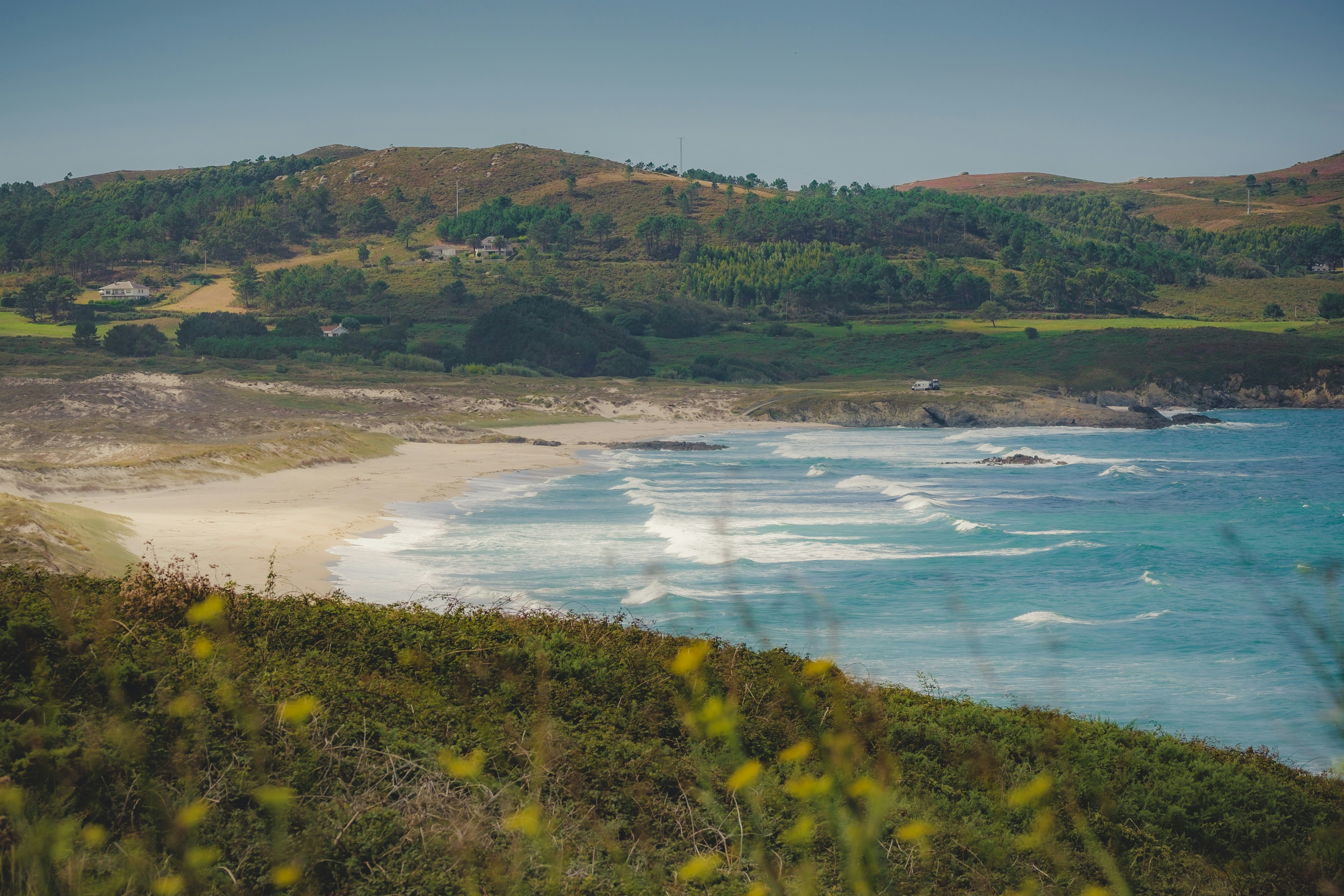 Serene beach scene with gentle waves lapping at the shore, framed by lush greenery and rolling hills in the background.