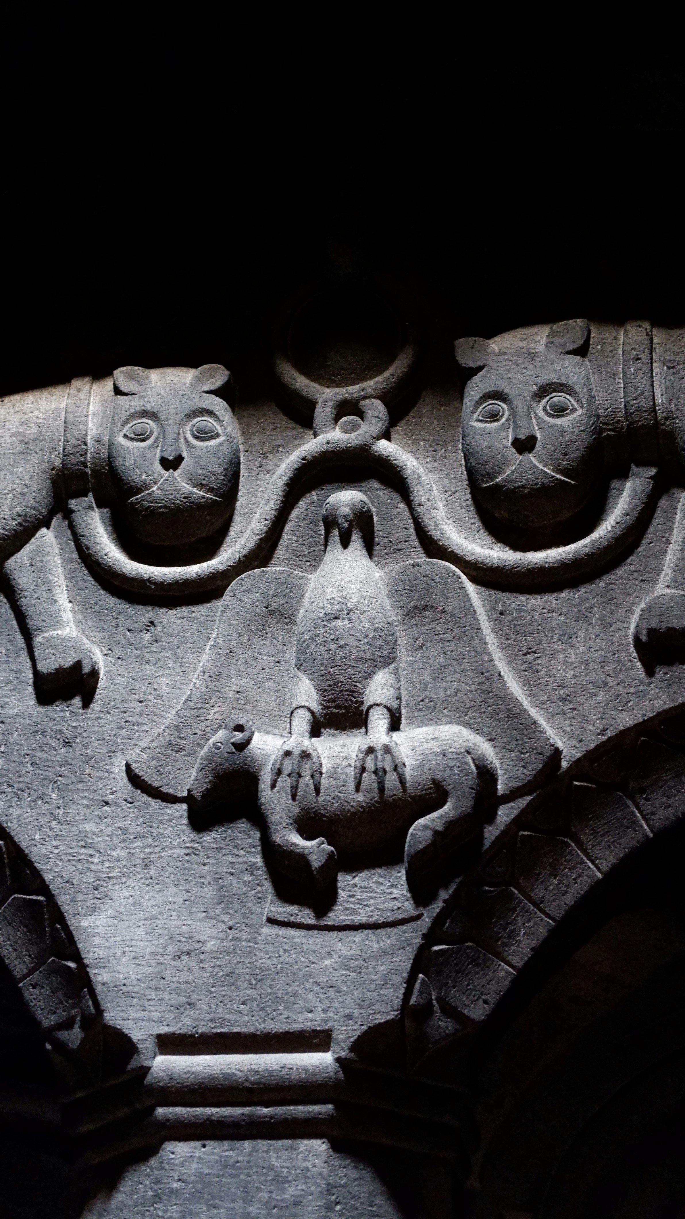 Guardians of the Crest: Twin Masks Framing a Central Avian Emblem in Stone