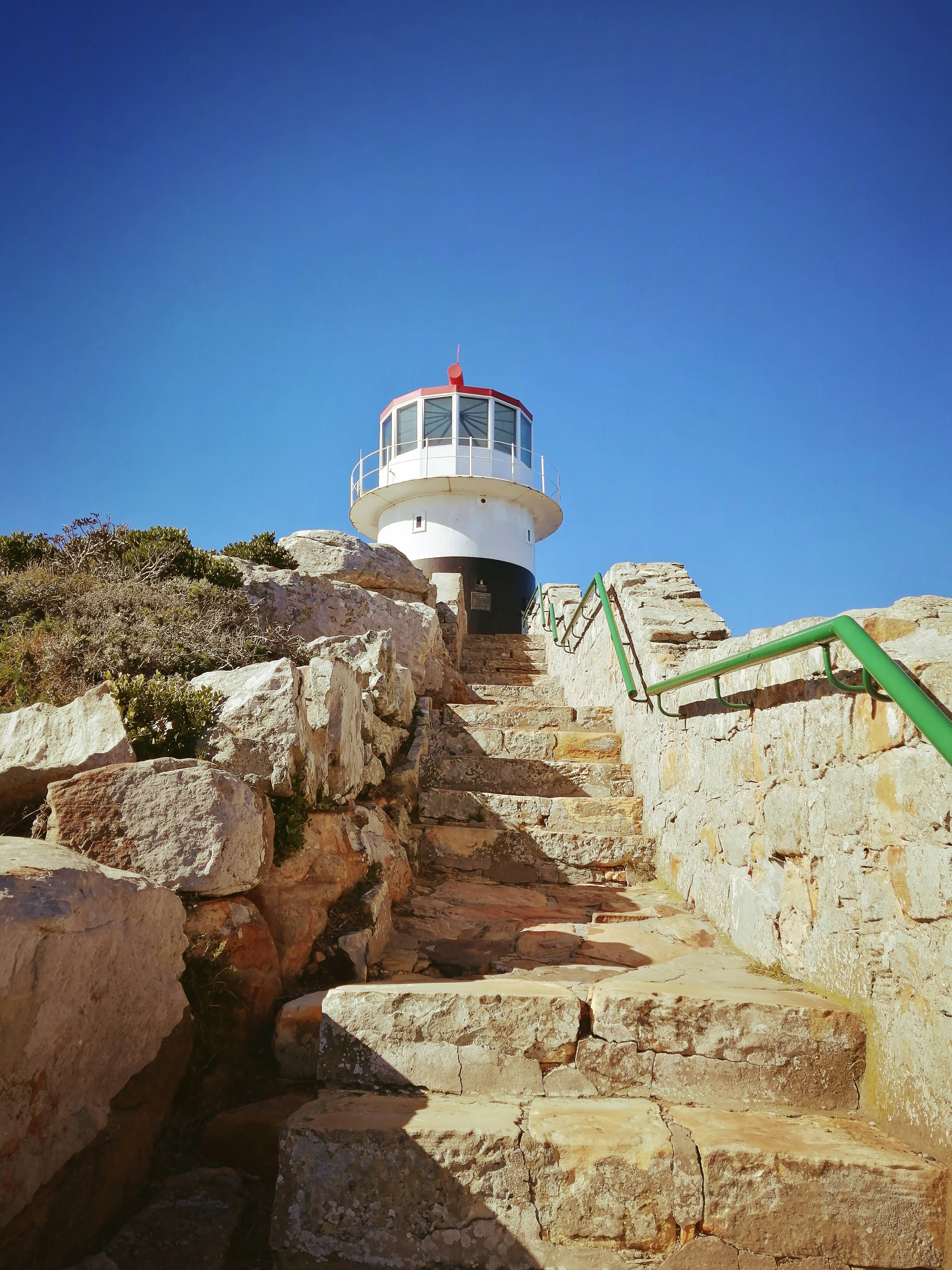 Stone steps leading up to a lighthouse, framed by rocky terrain and clear blue skies.