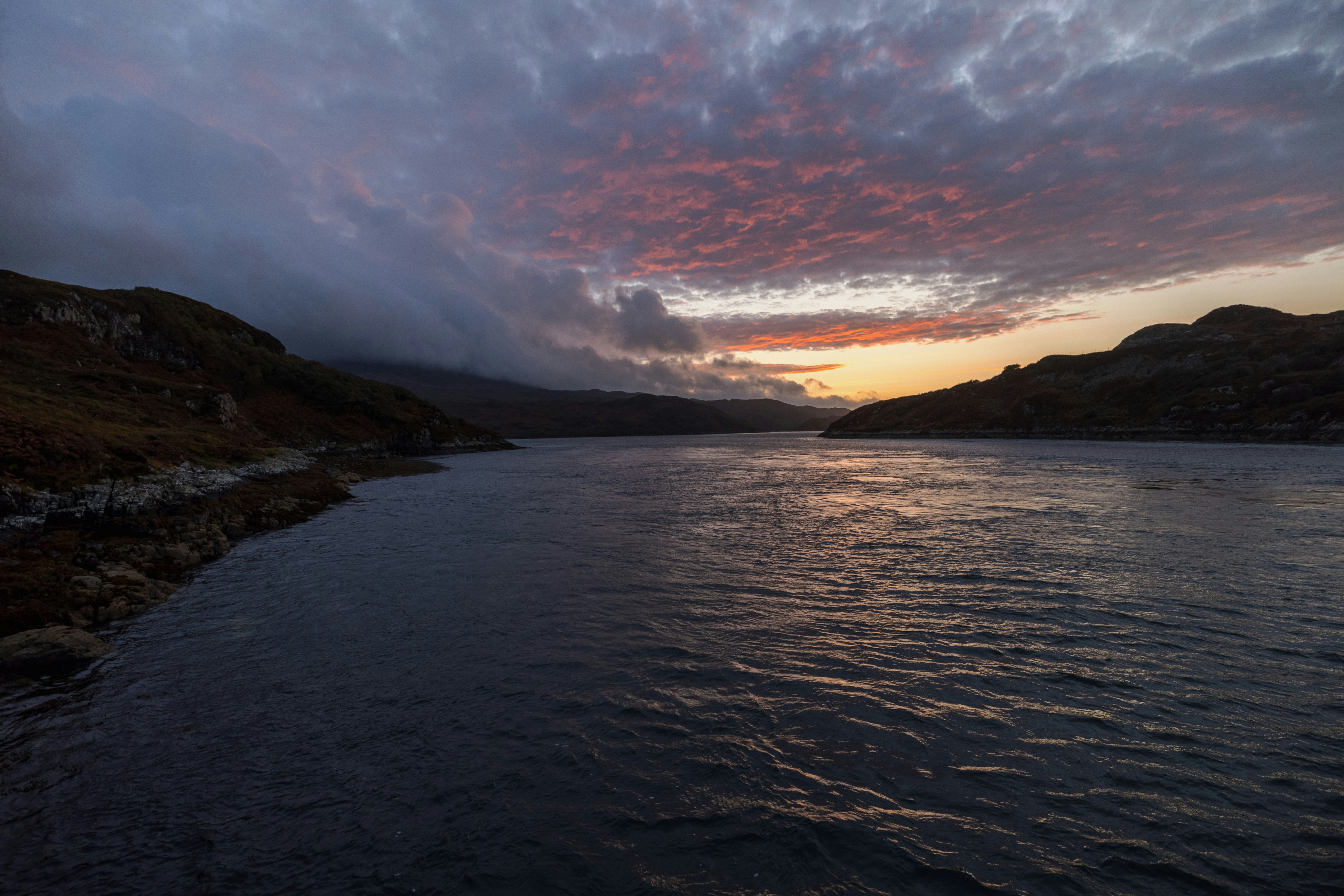 a body of water surrounded by mountains under a cloudy sky