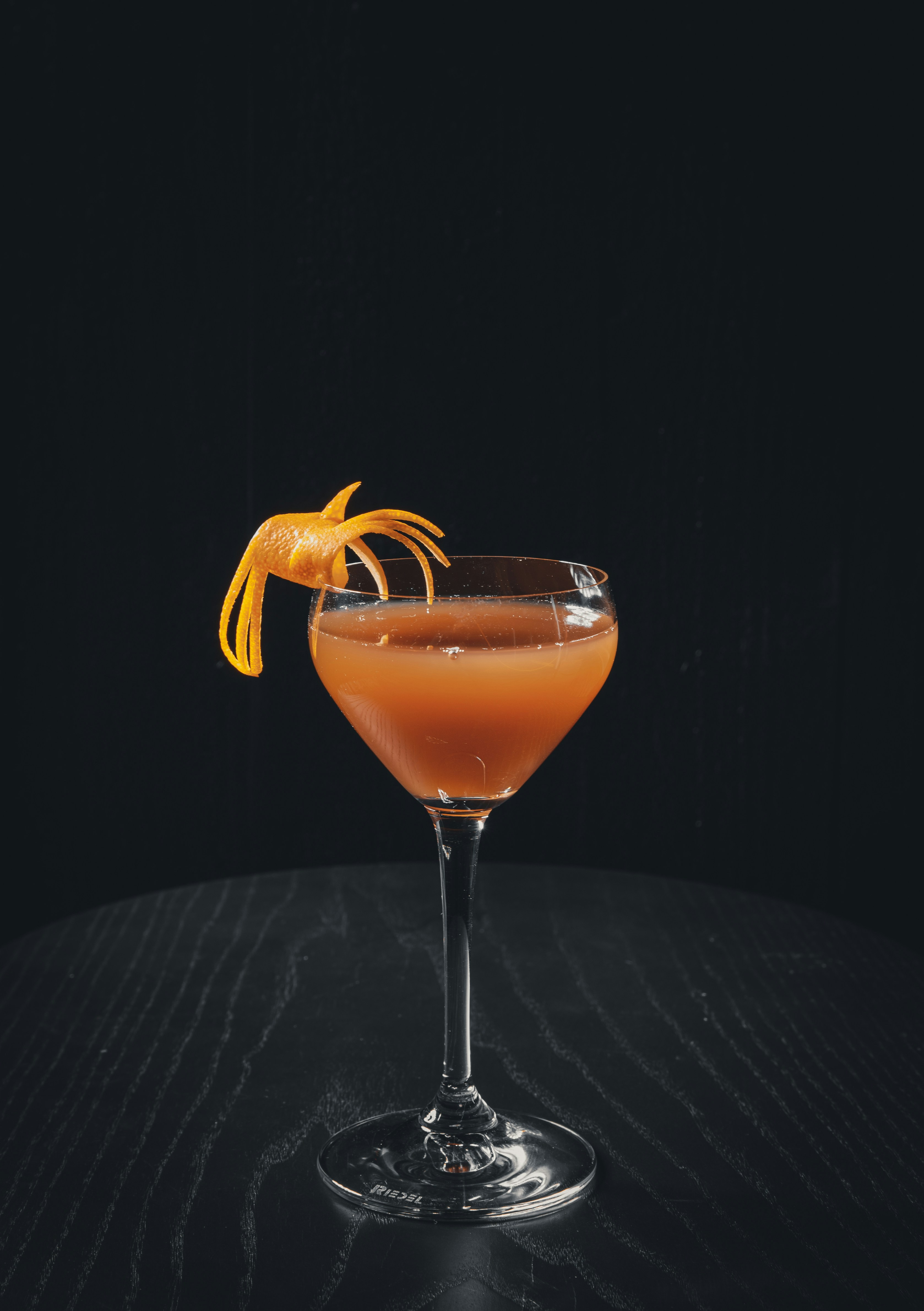 A cocktail garnished with a vibrant orange twist sits elegantly in a classic glass against a dark backdrop.
