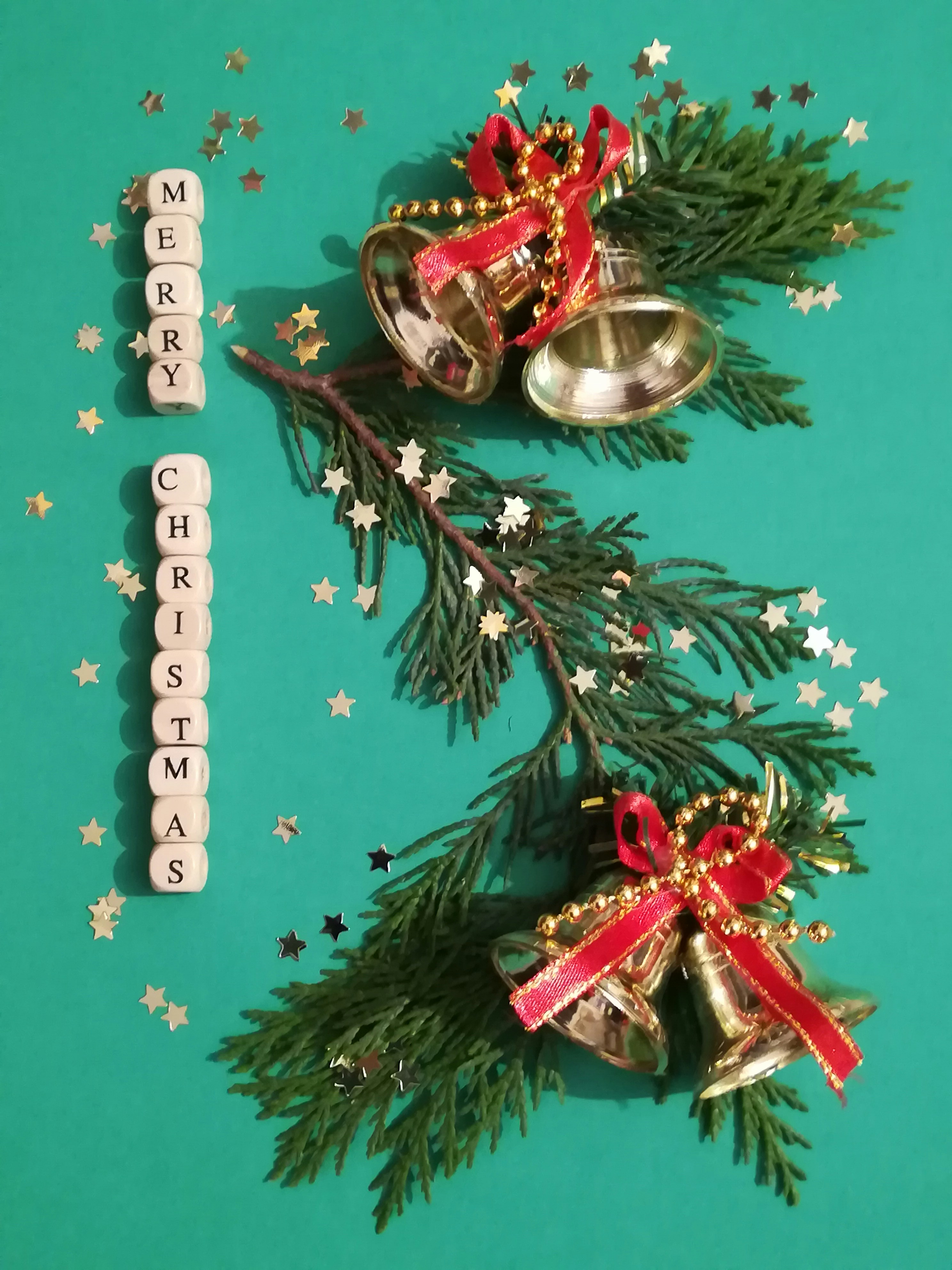 Gold bells adorned with red ribbons and a green pine branch, surrounded by festive stars and letter blocks spelling 'MERRY CHRISTMAS'.