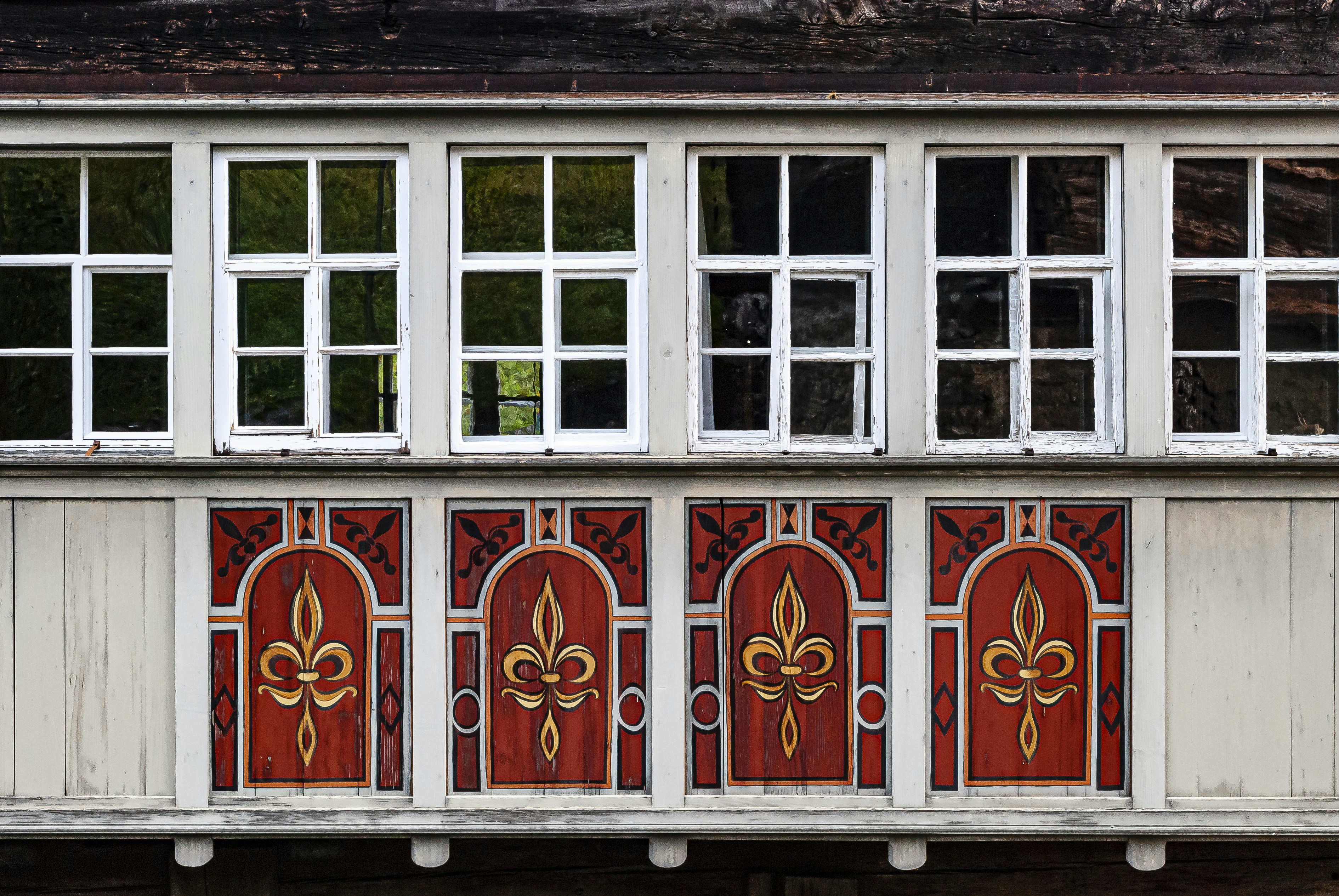 Crimson Doors: Fleur-de-lis Symmetry Beneath a Windowed Frieze