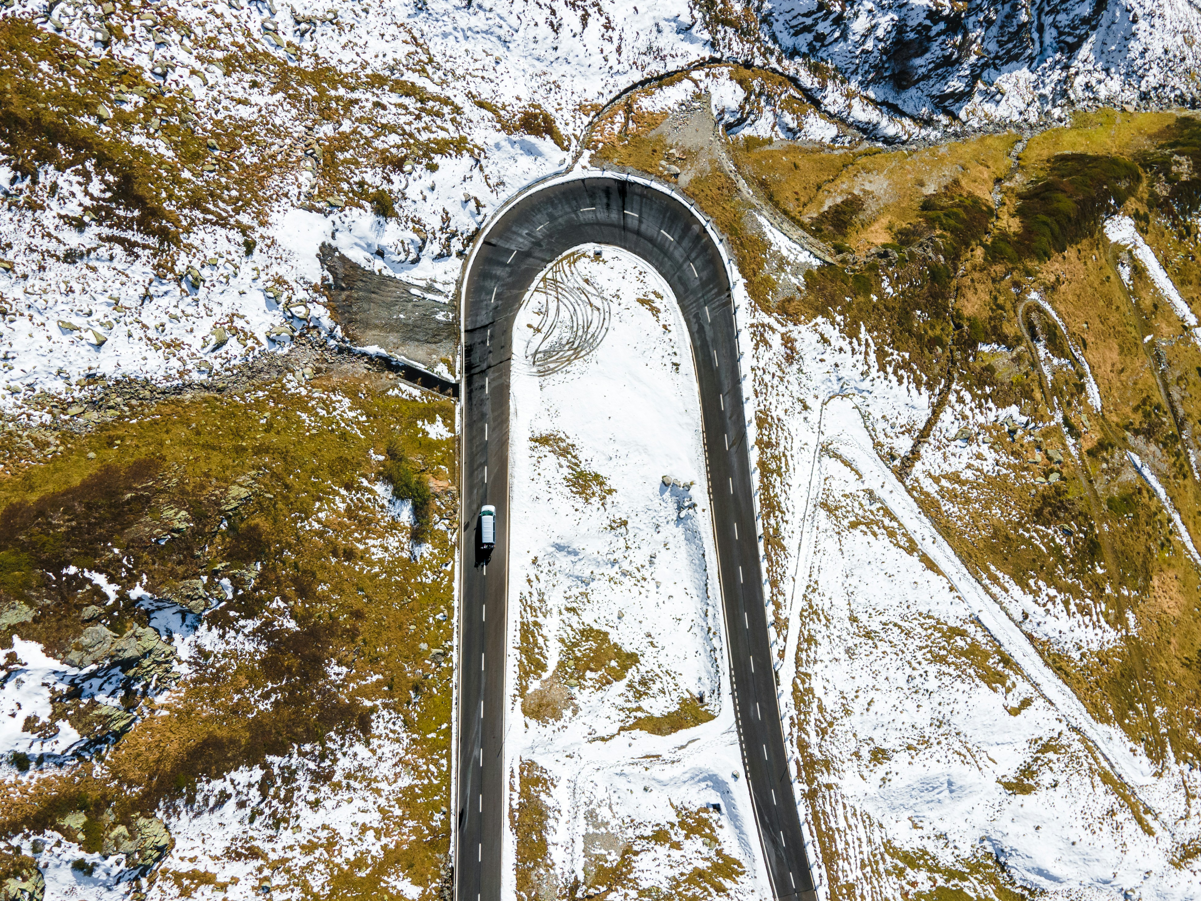 Curved road bridge arches over a snow-dusted valley, captured from above in a high-altitude drone photograph.