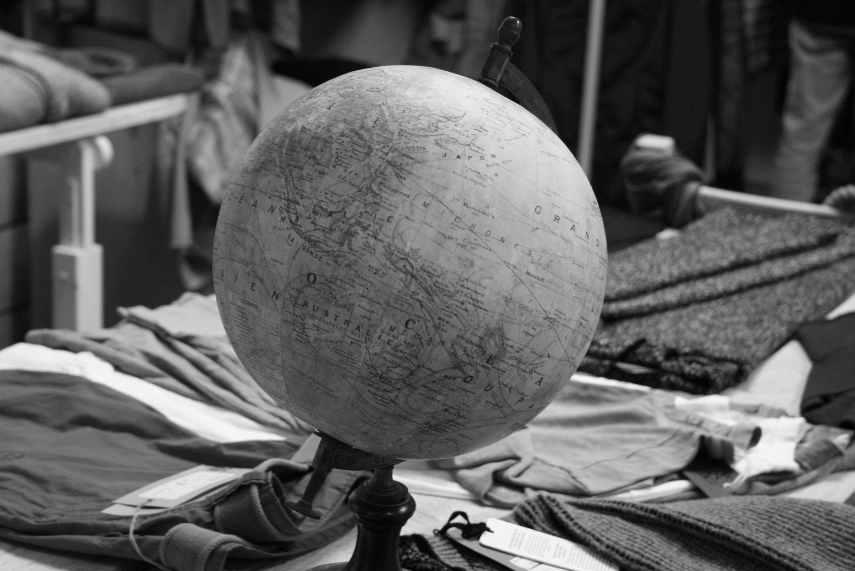 Vintage globe resting on a table surrounded by fabric and clothing items, showcasing intricate map details.