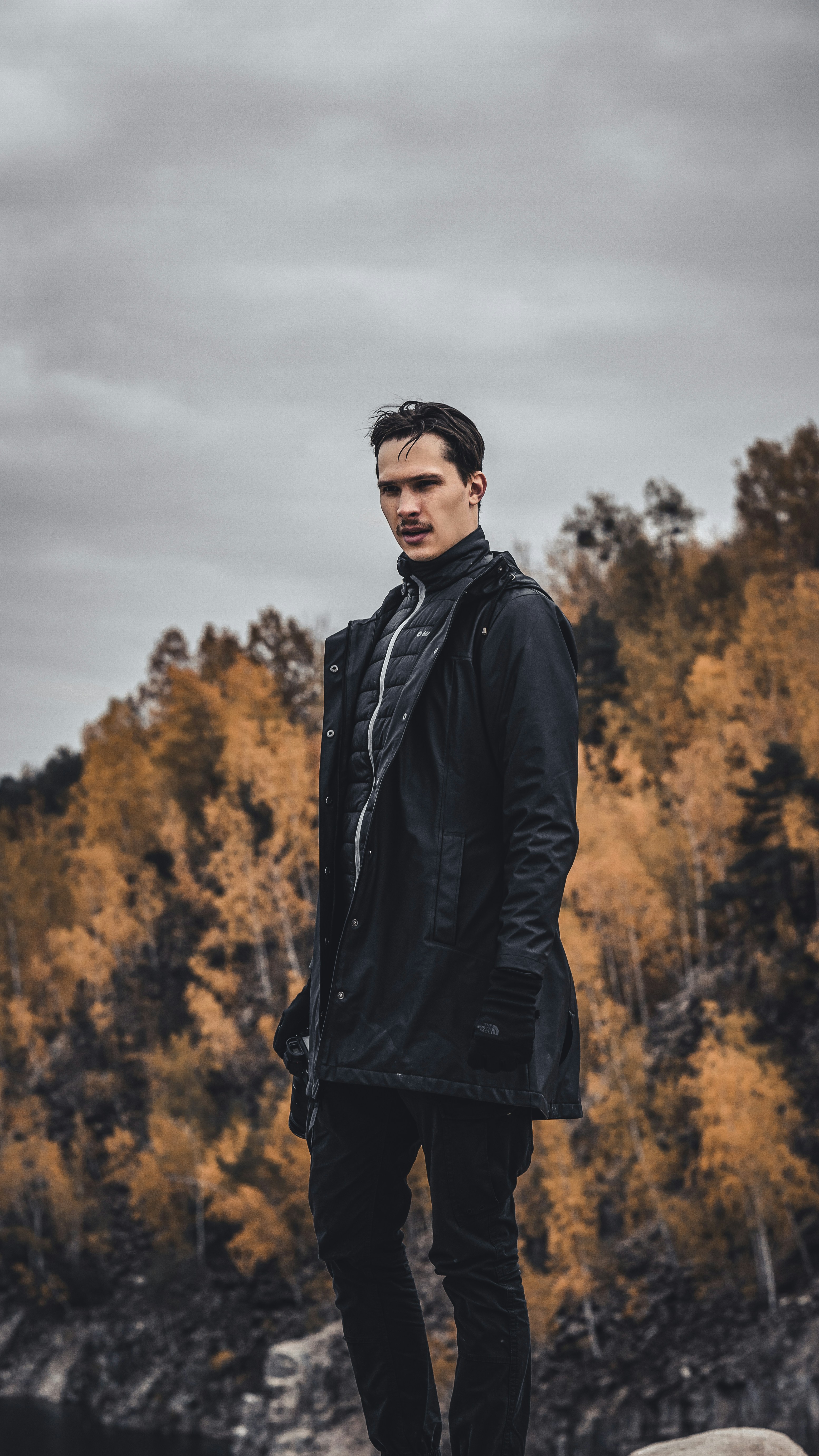 Quiet Stand in Copper Woods: A lone man in a black parka framed by autumn amber trees