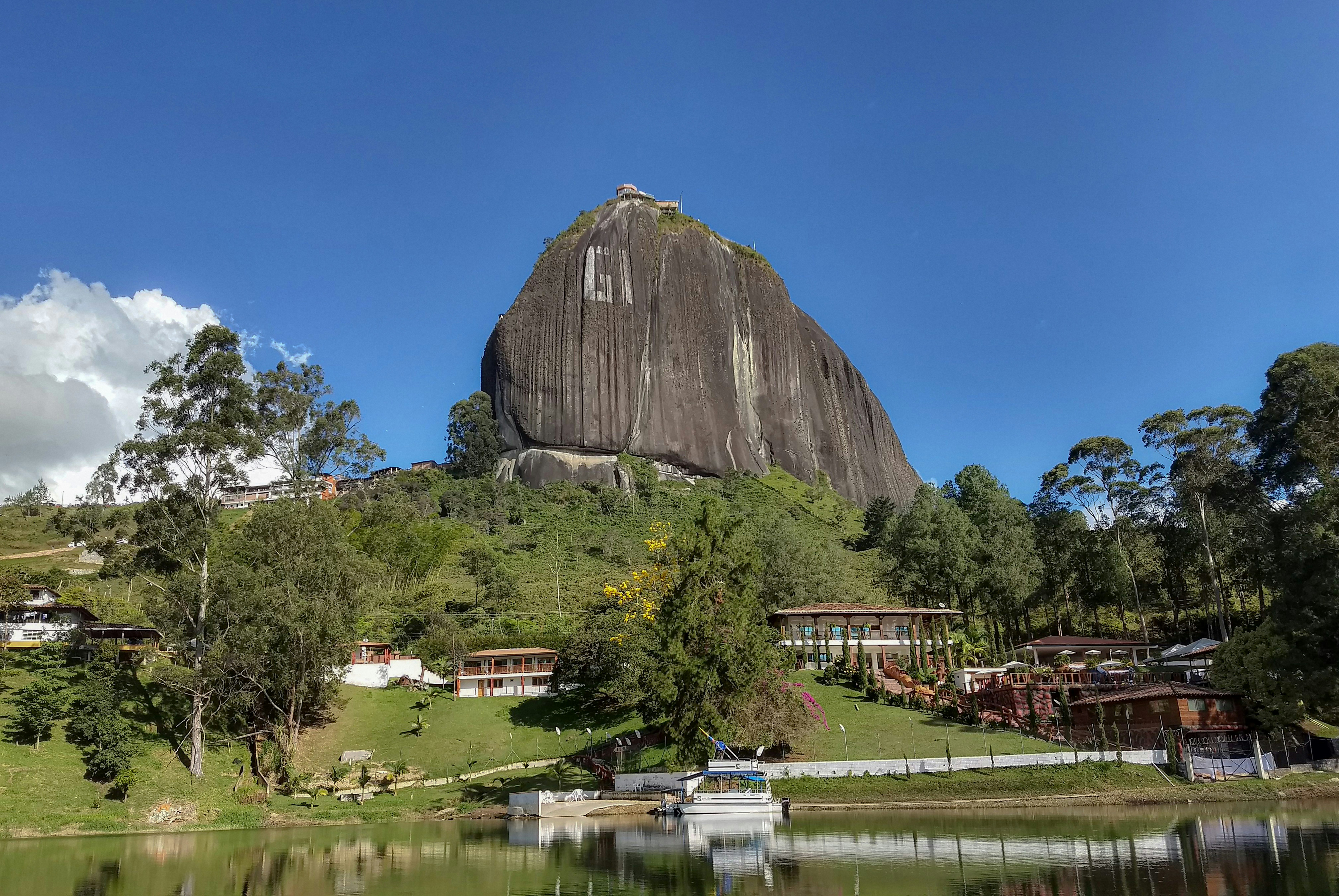 Massive rock formation towers over a lush, green hillside beneath a clear blue sky.