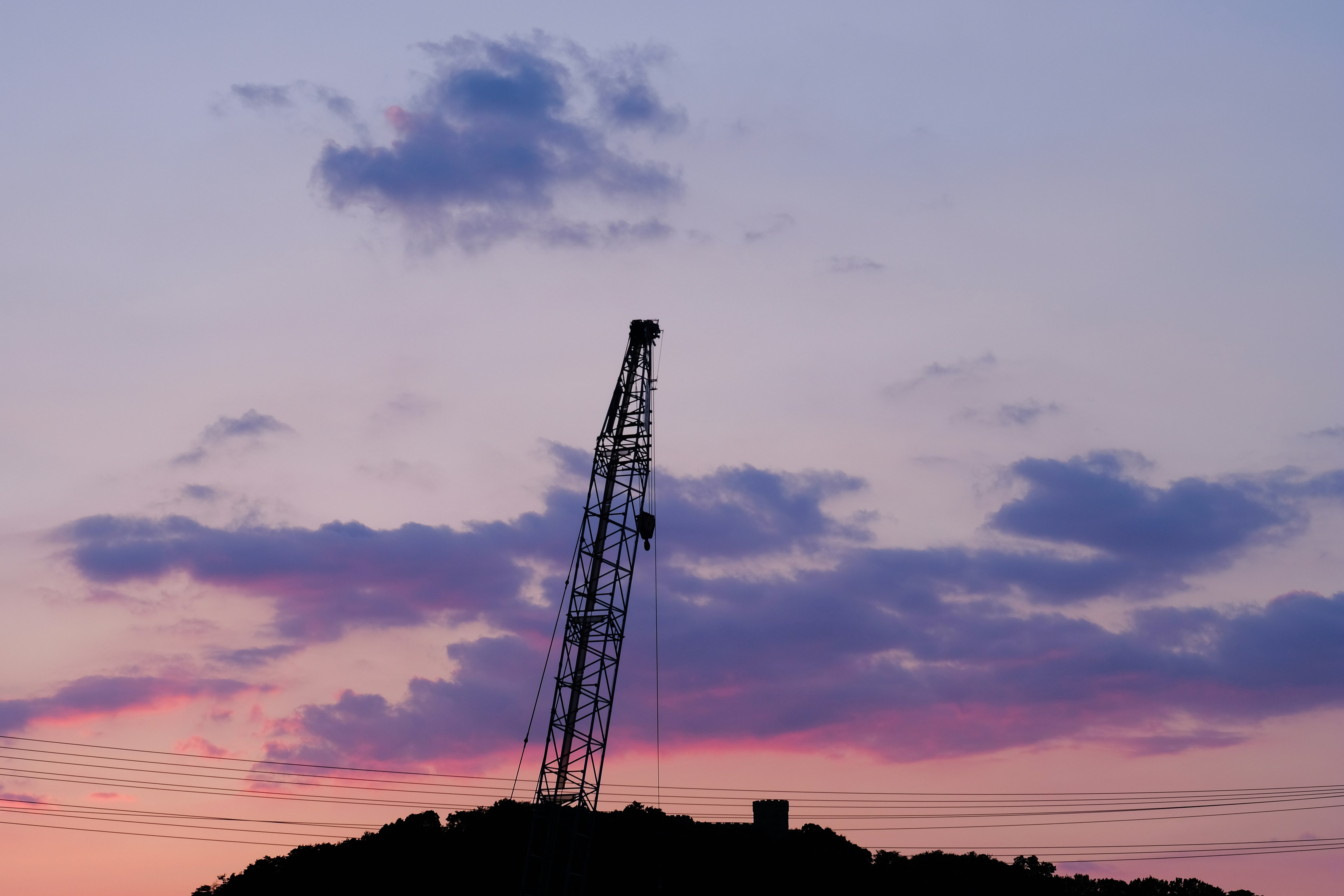 Silhouette of a construction crane against a pastel sky during sunset, highlighting the transition from day to night.