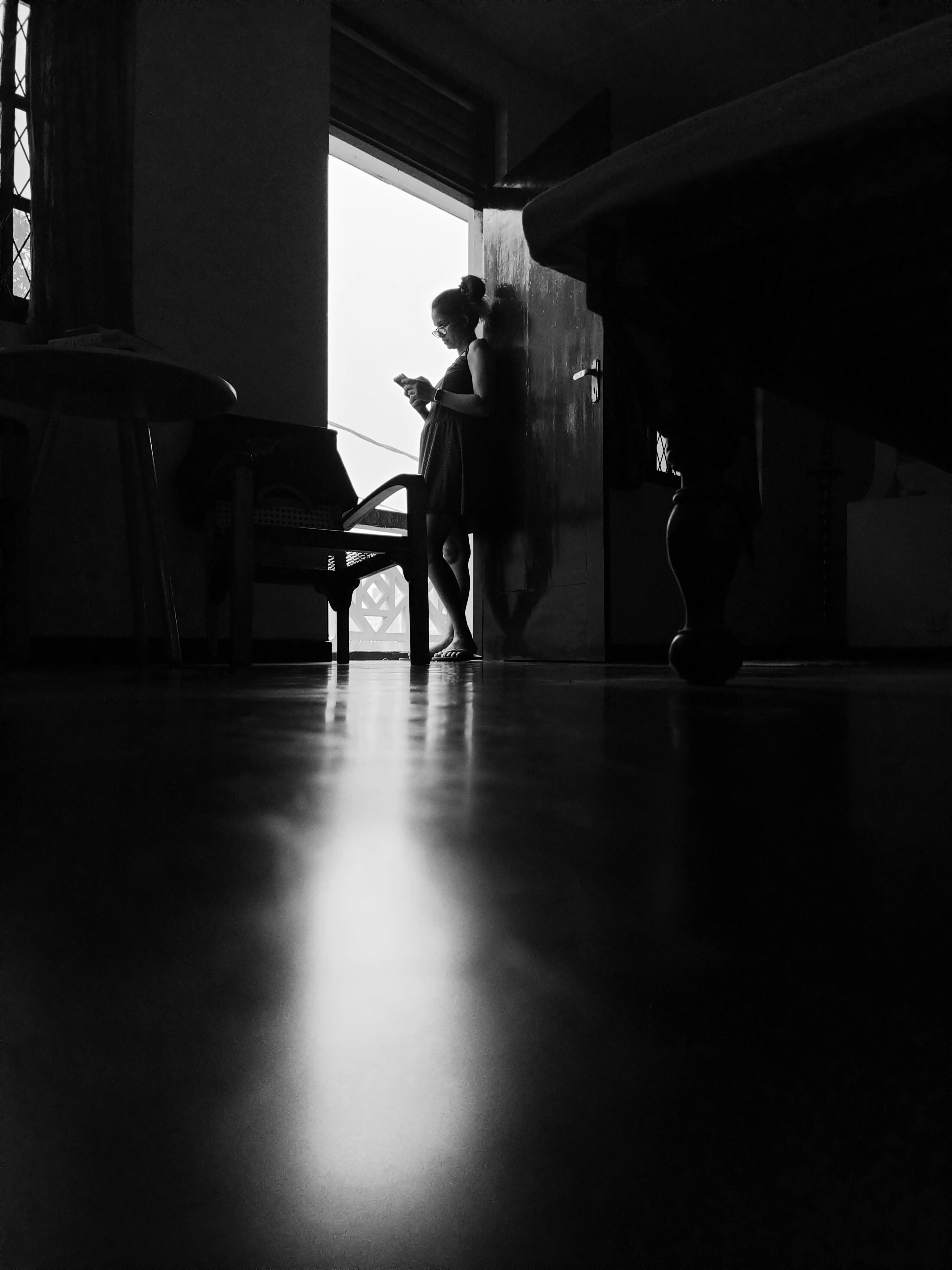 Silhouette of a person standing by a doorway in a dimly lit room with reflective flooring.
