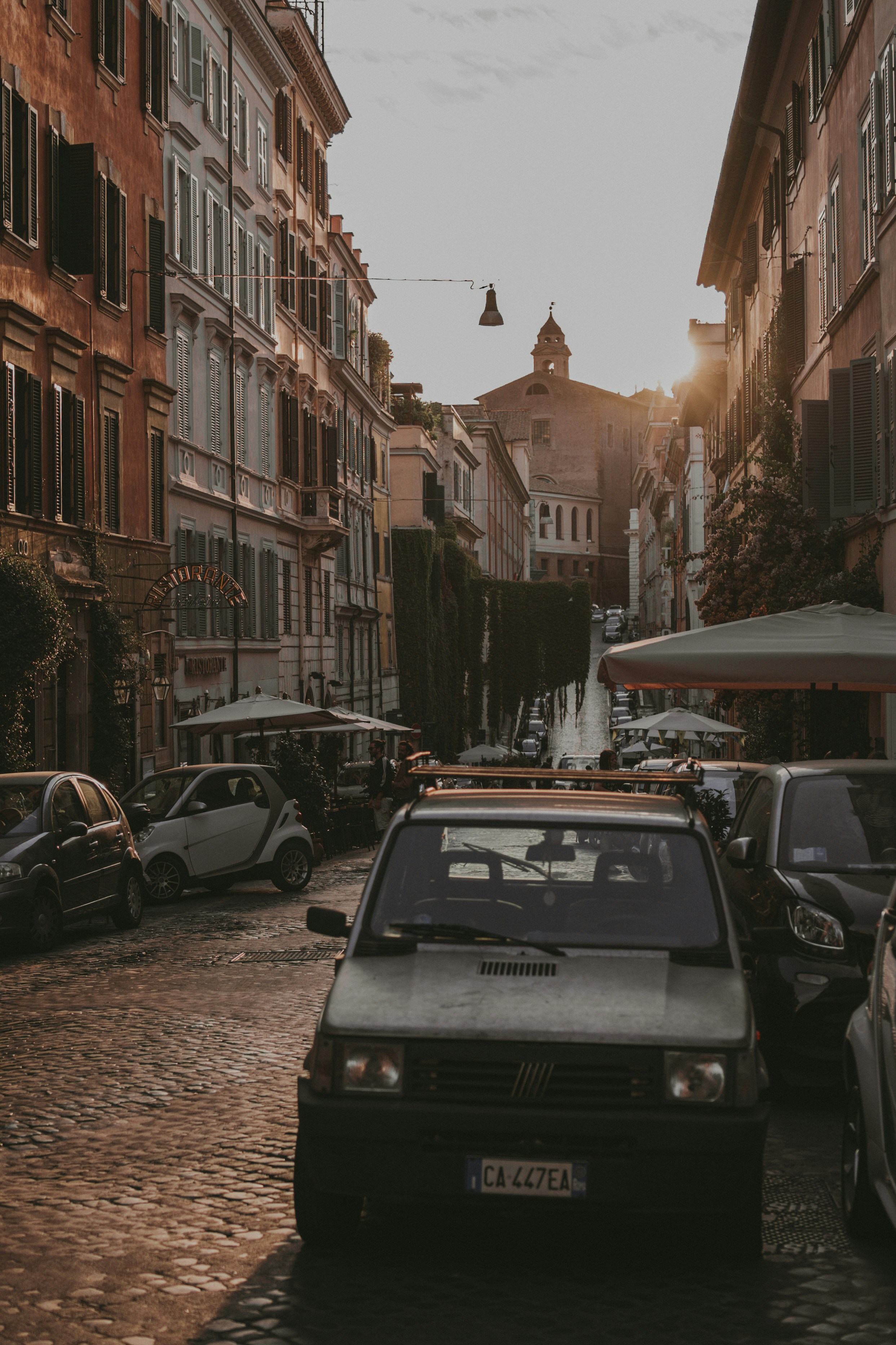 Golden Hour on a European Cobblestone Street: A Van Framed by Brick Facades and a Distant Dome