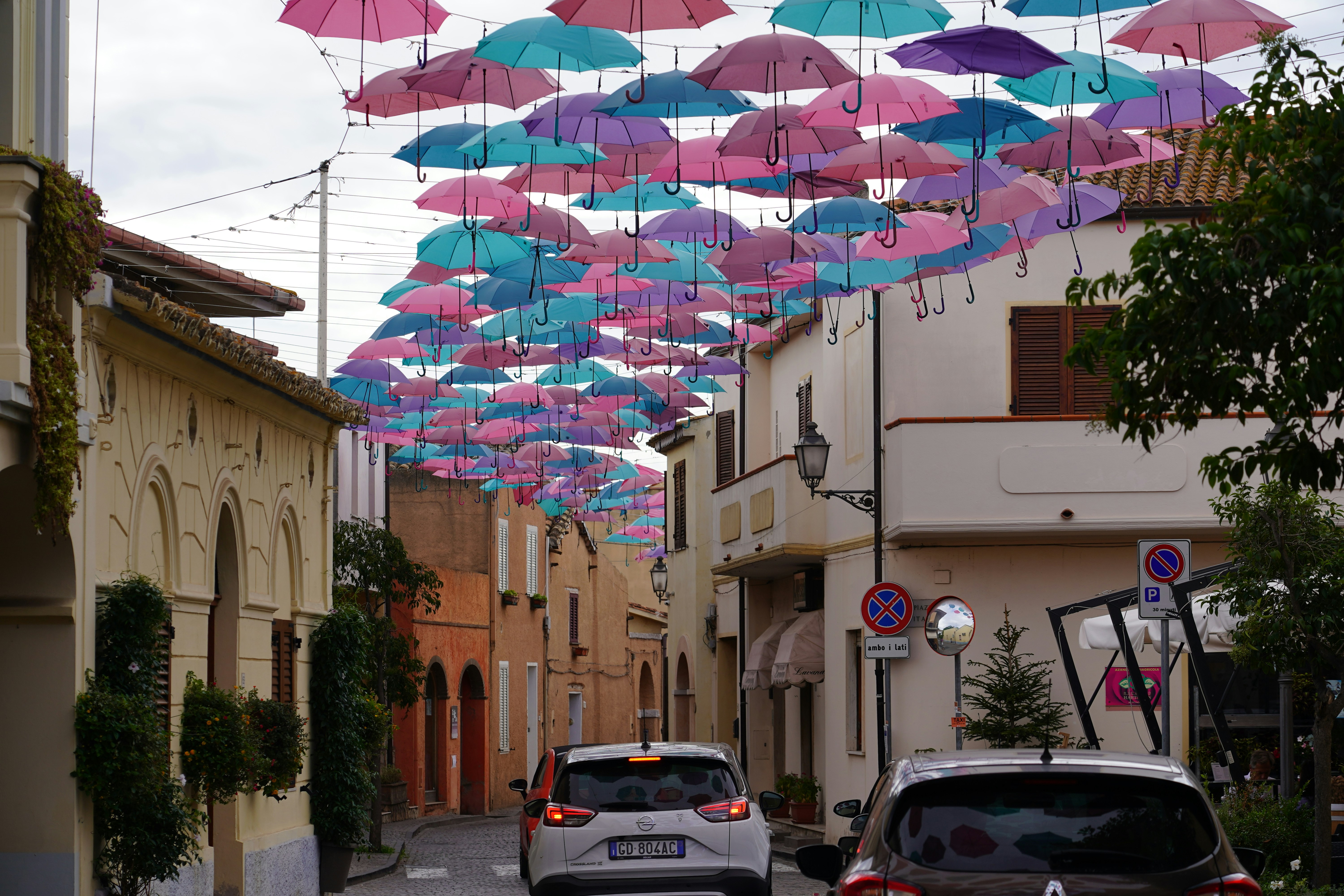 Colorful umbrellas suspended above a narrow street lined with charming buildings and parked cars.