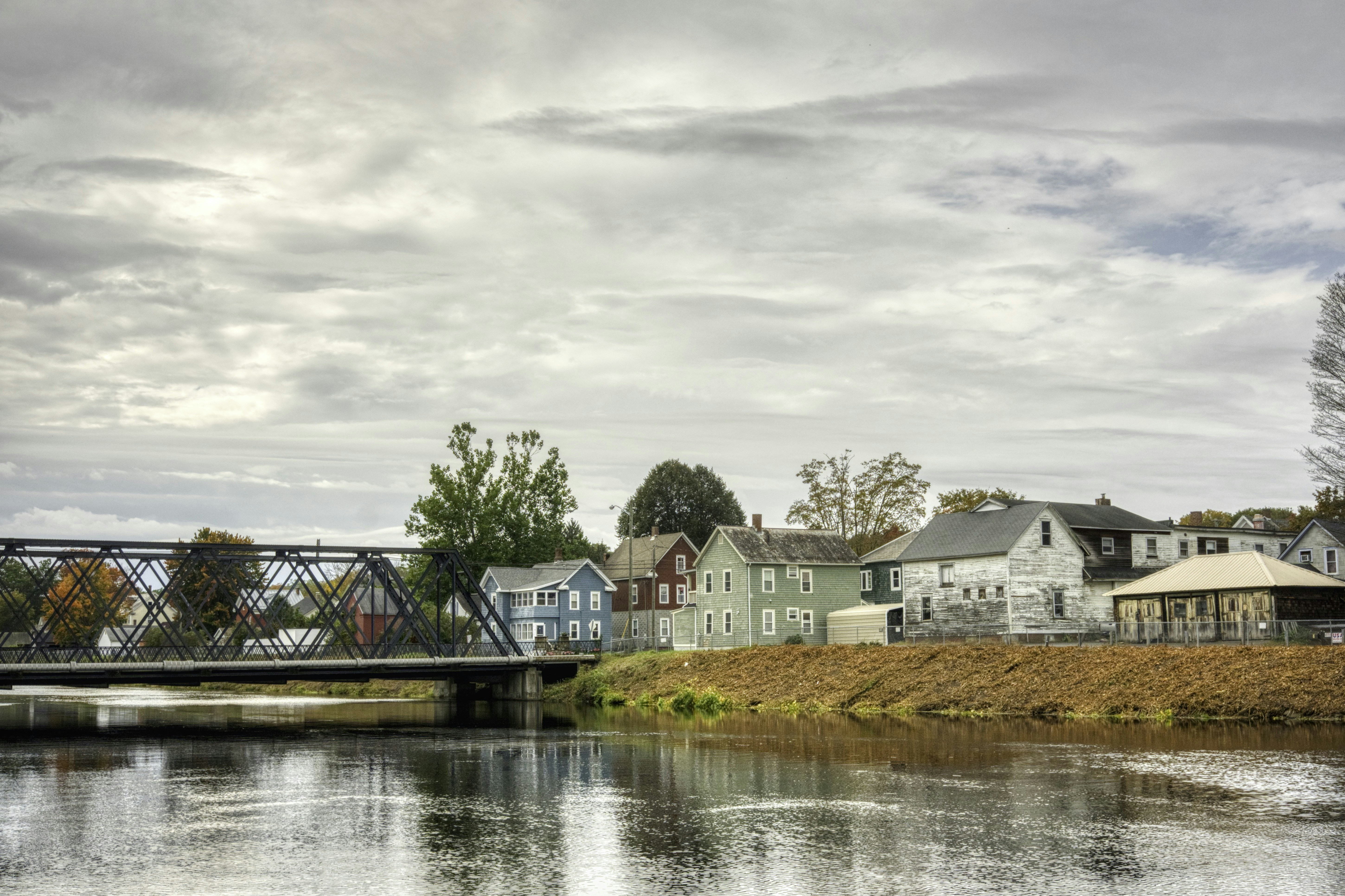 Charming riverside houses reflect in calm waters beneath an overcast sky, showcasing a tranquil community vibe.