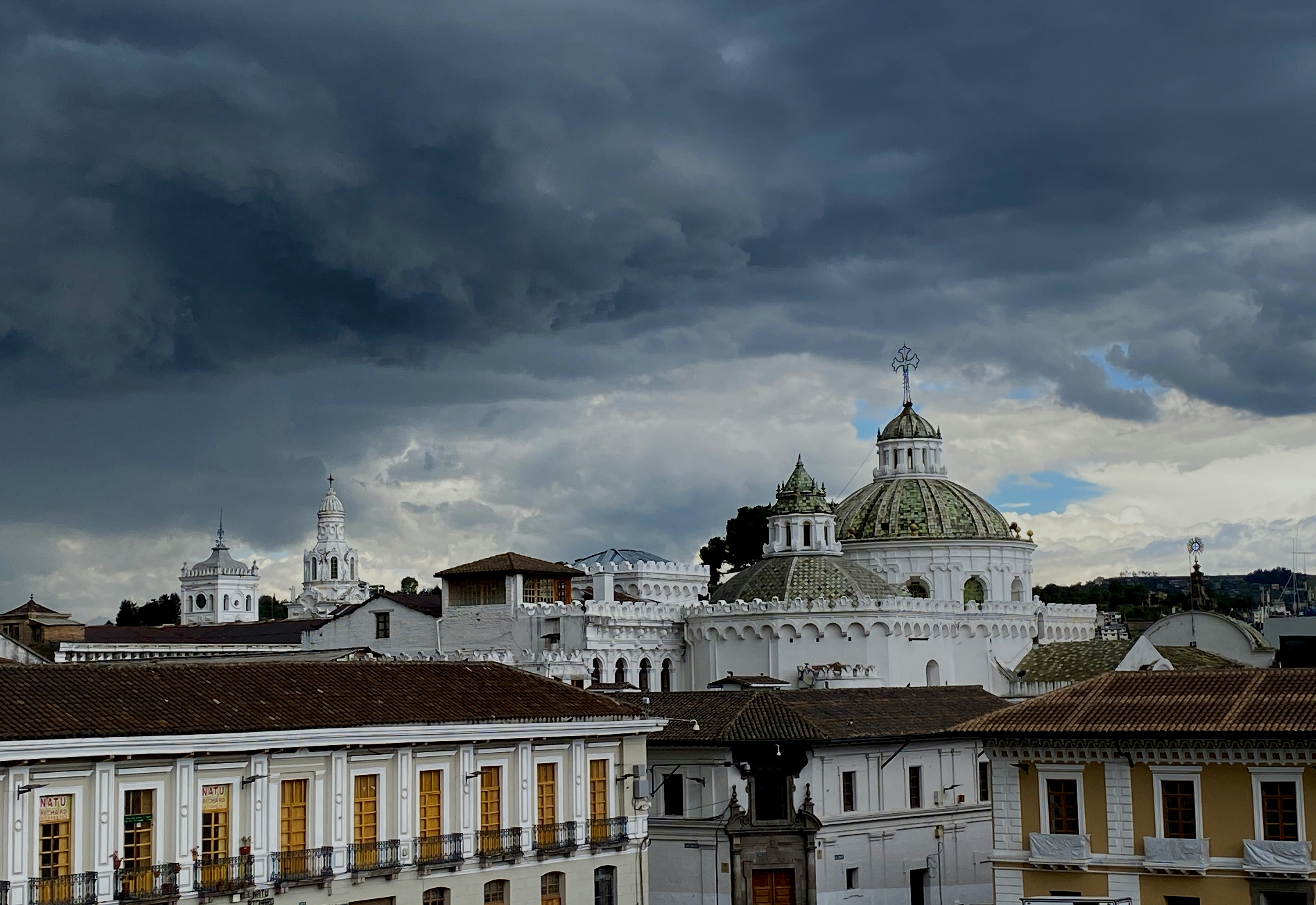 Dramatic clouds loom over ornate historic buildings with domed rooftops.