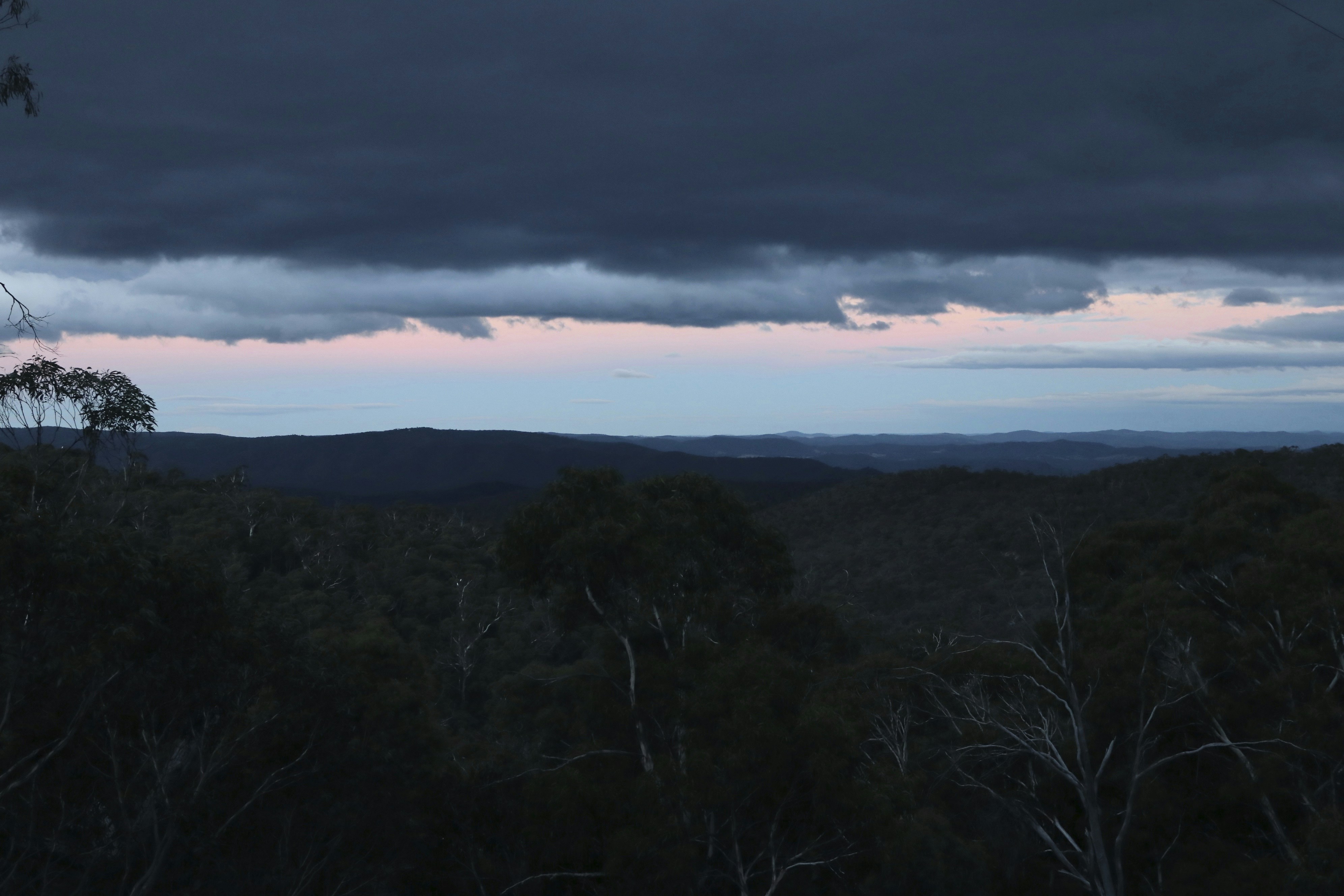 Dark clouds loom over rolling hills at dusk, with a faint pink glow on the horizon.