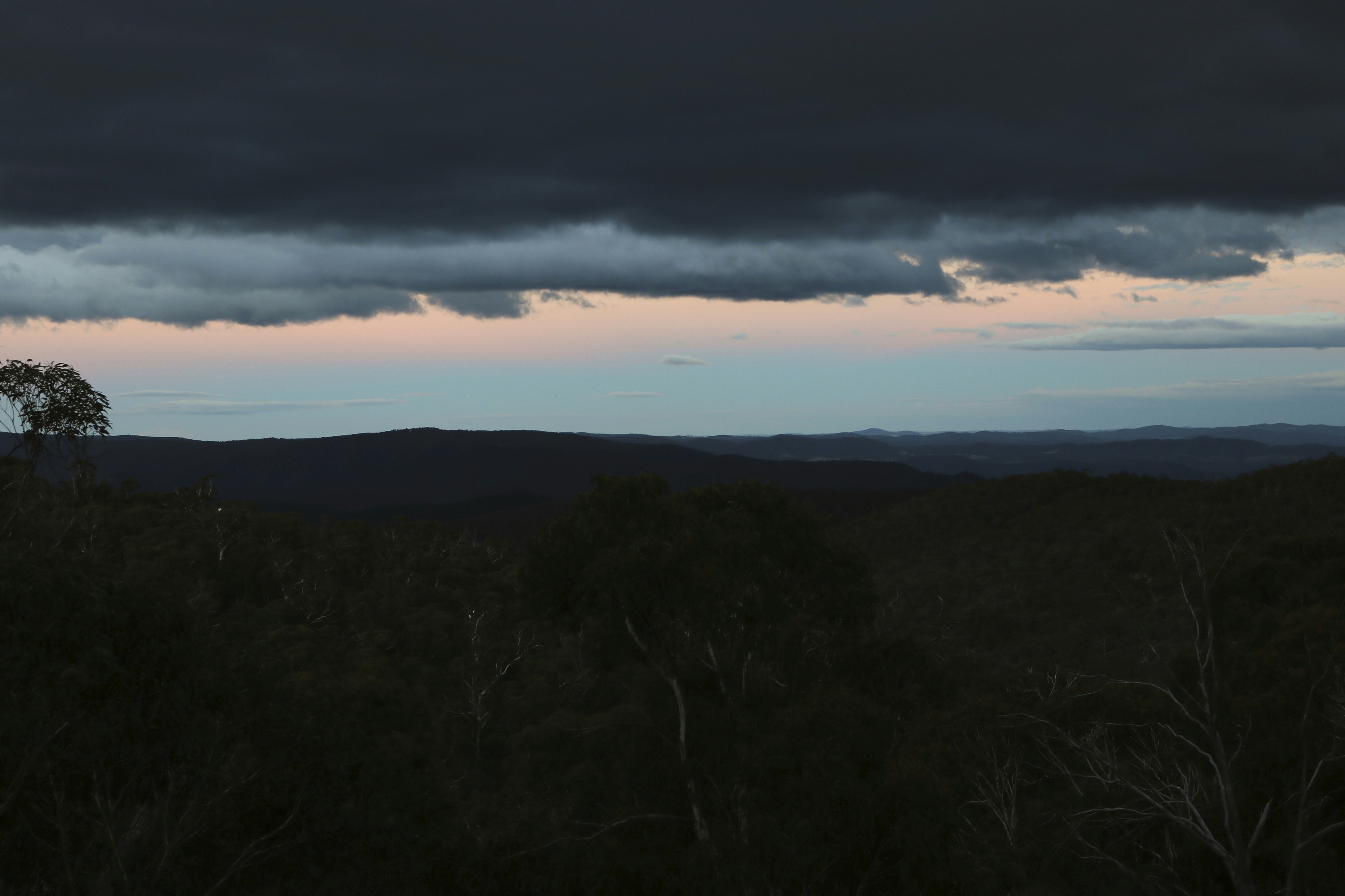 Dramatic clouds loom over a distant mountain range, with a subtle gradient of color marking the horizon. The scene captures the tranquil yet foreboding essence of twilight.