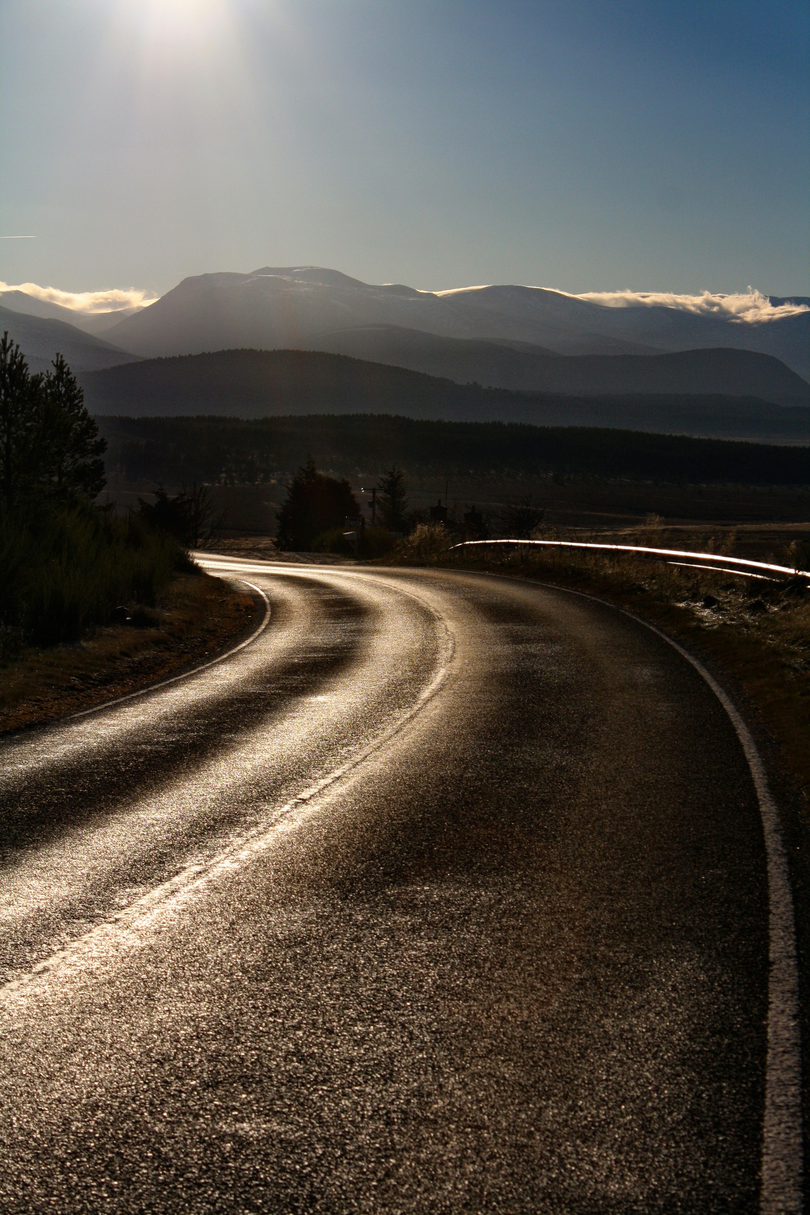 Sunlit winding road leading towards distant mountains under a clear sky.