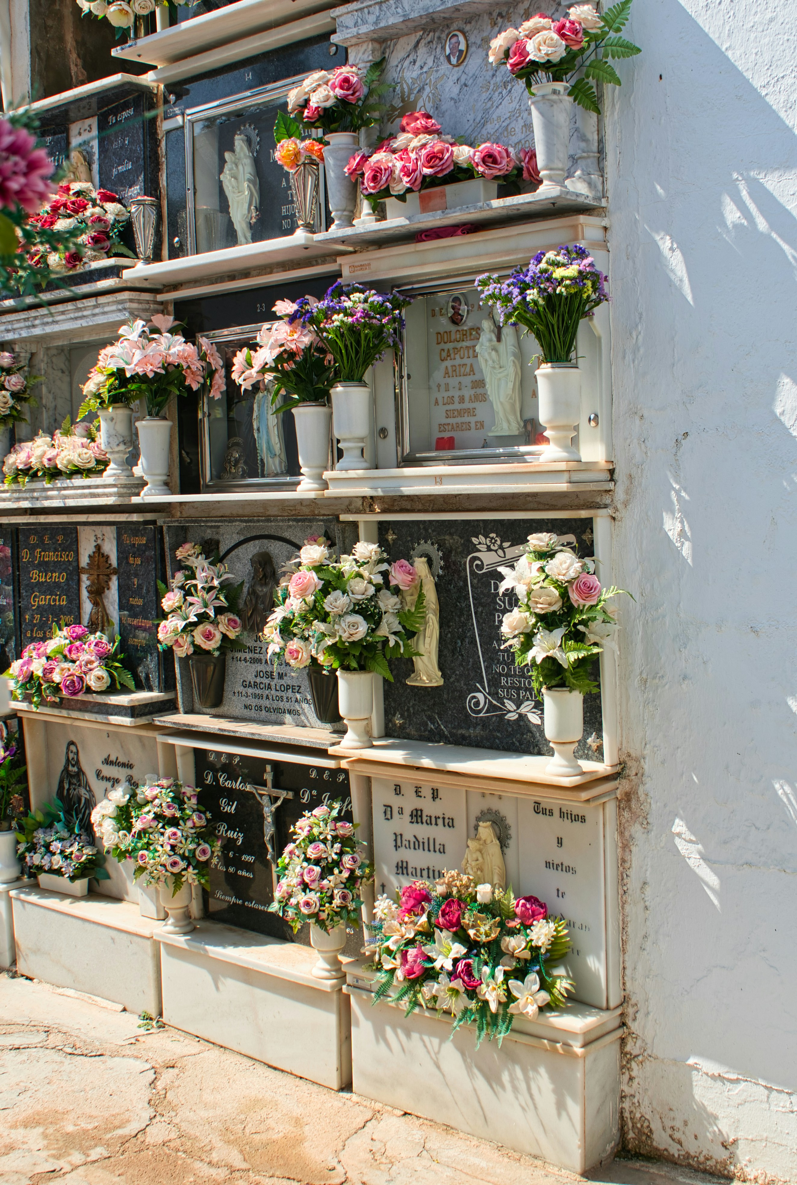 A serene cemetery wall adorned with floral arrangements and memorial plaques, reflecting a blend of remembrance and beauty.