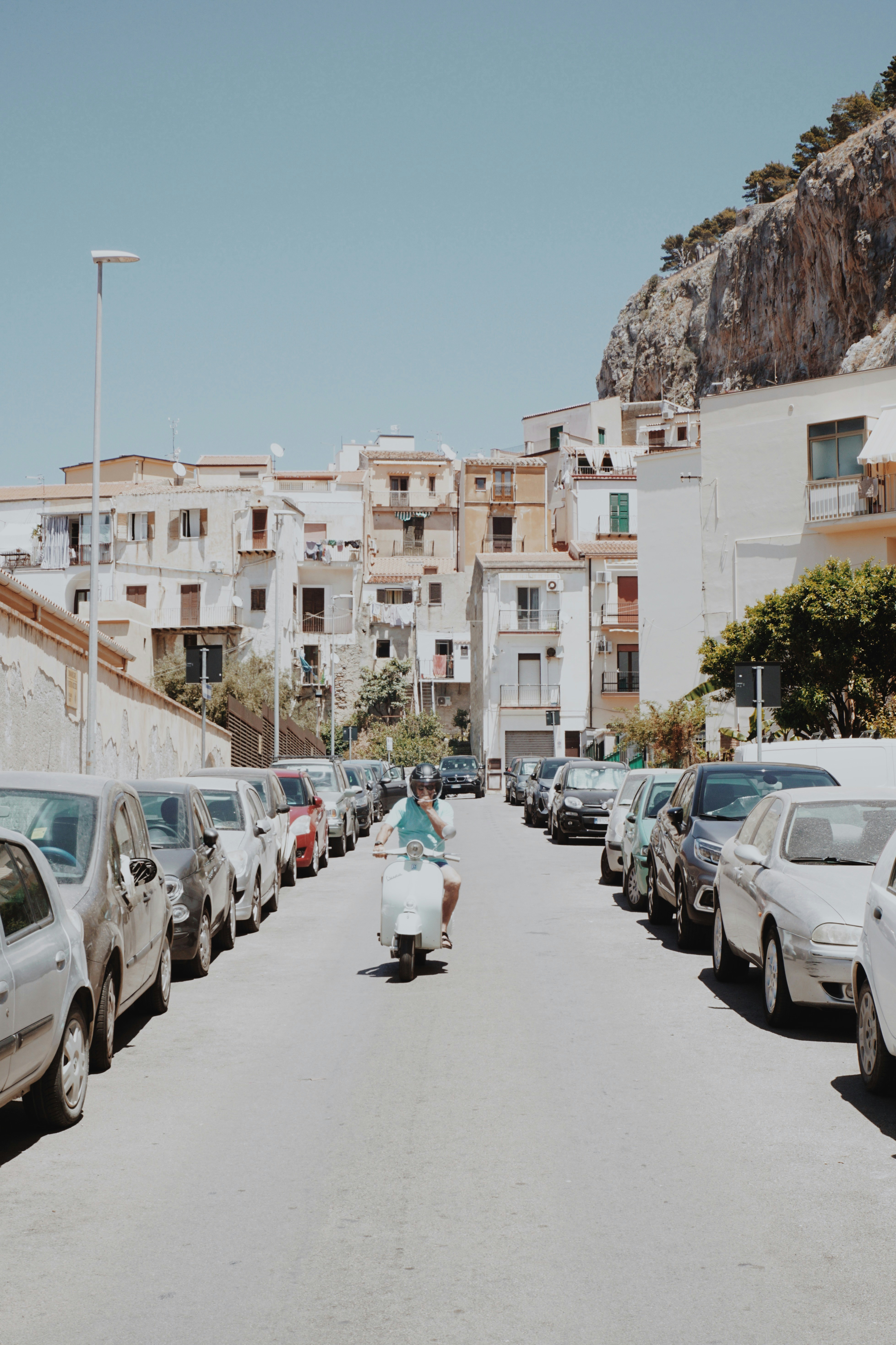 Sunlit Mediterranean Street: a lone scooter threads a car-lined boulevard