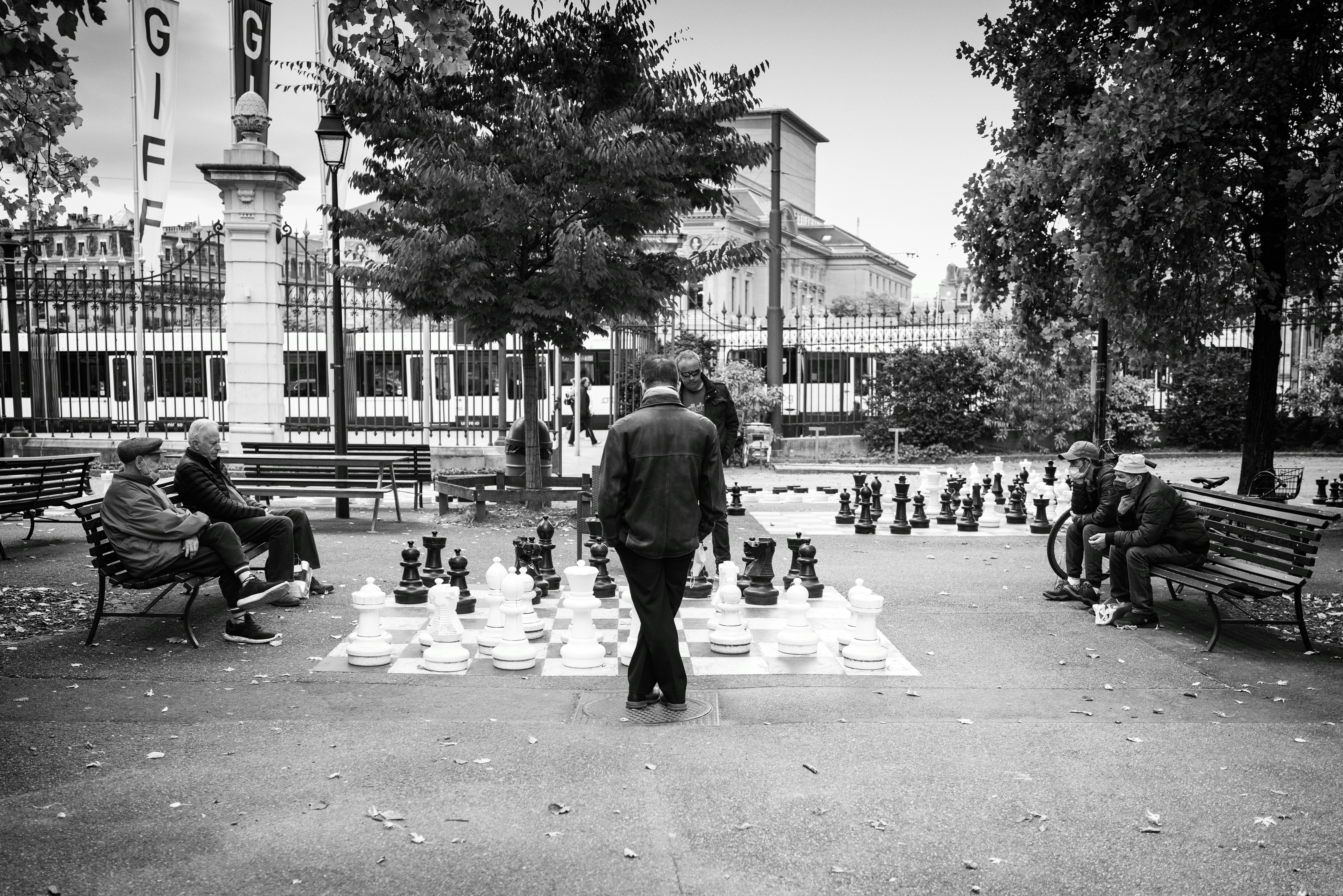Men engaged in a game of chess in a park, surrounded by large chess pieces and benches. The scene captures the essence of leisure and strategy.