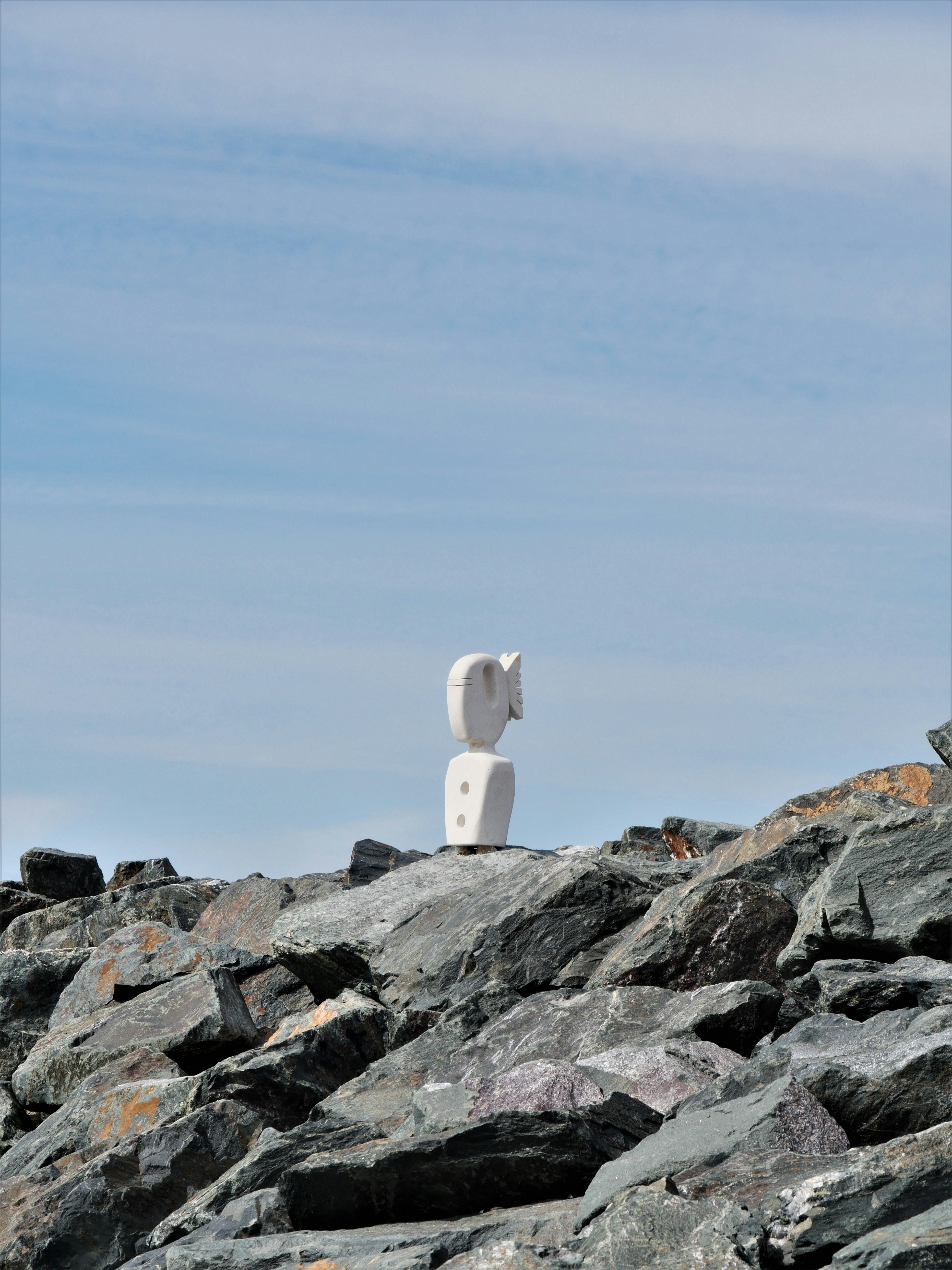 A minimalist sculpture stands atop a rocky landscape under a clear sky, embodying a blend of art and nature.