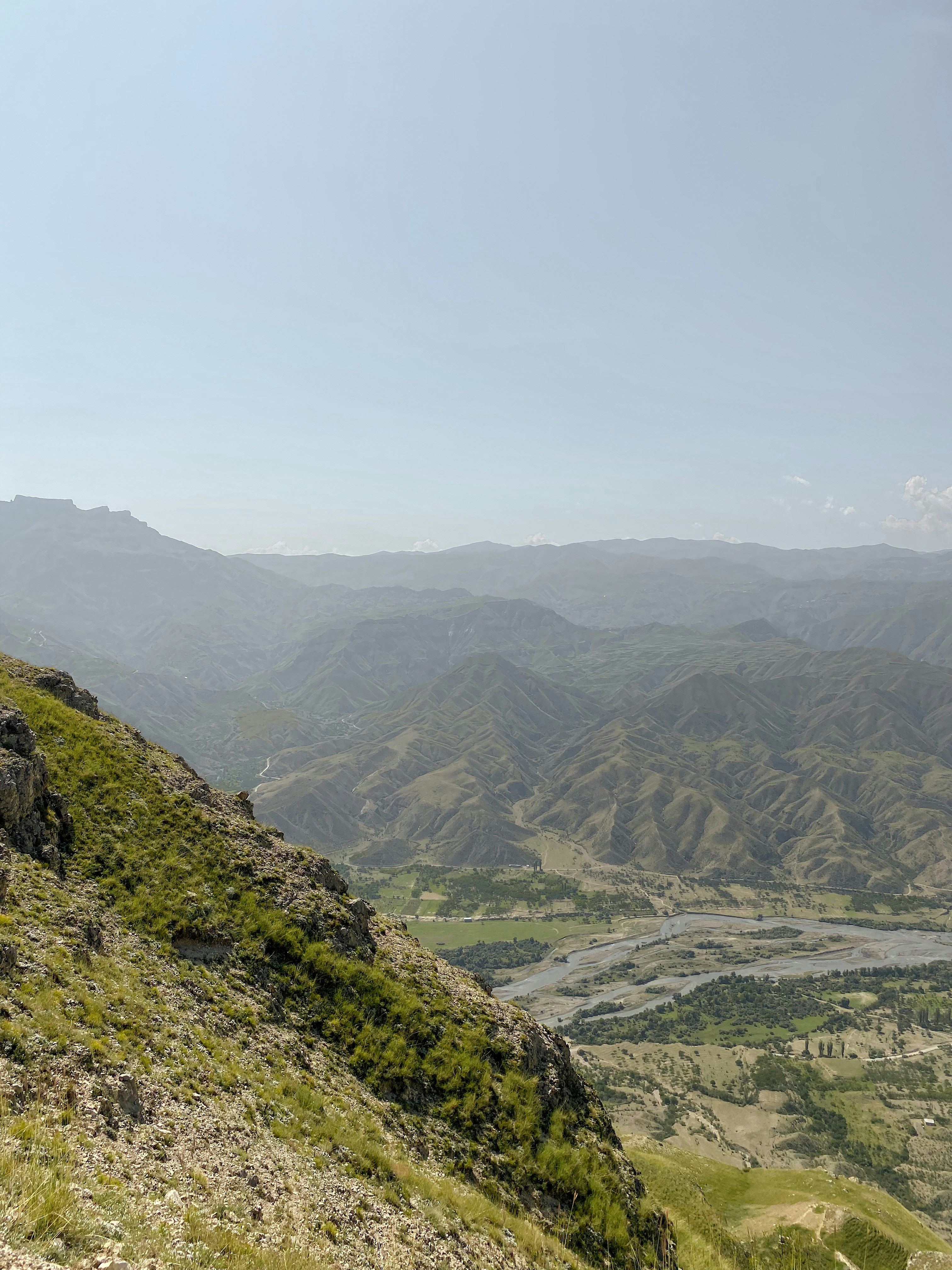 Expansive view of rolling hills and valleys under a clear sky, showcasing the natural beauty of the terrain. A rocky outcrop in the foreground adds depth to the scene.