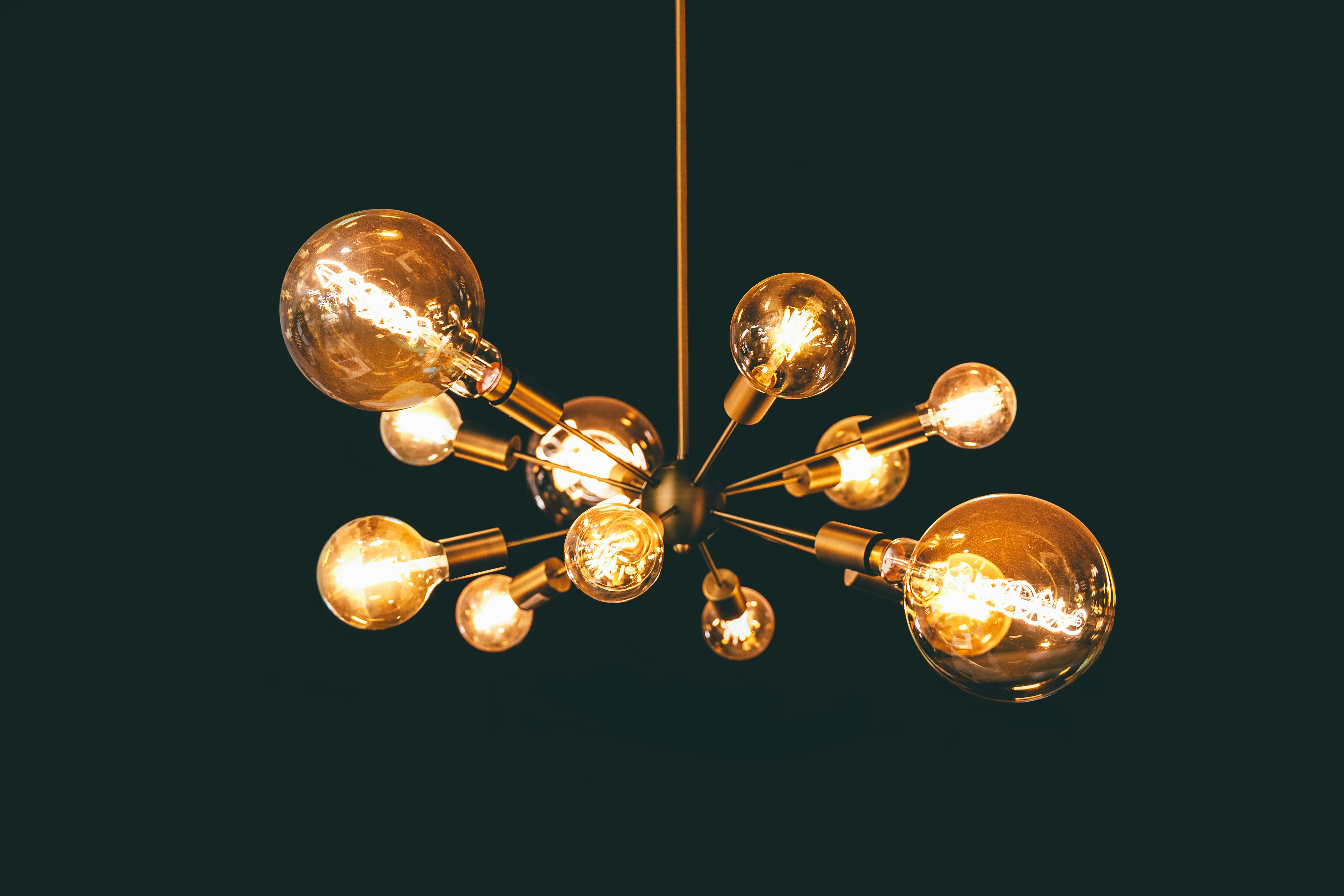 A modern chandelier featuring multiple light bulbs arranged in a dynamic, star-like formation against a dark background.