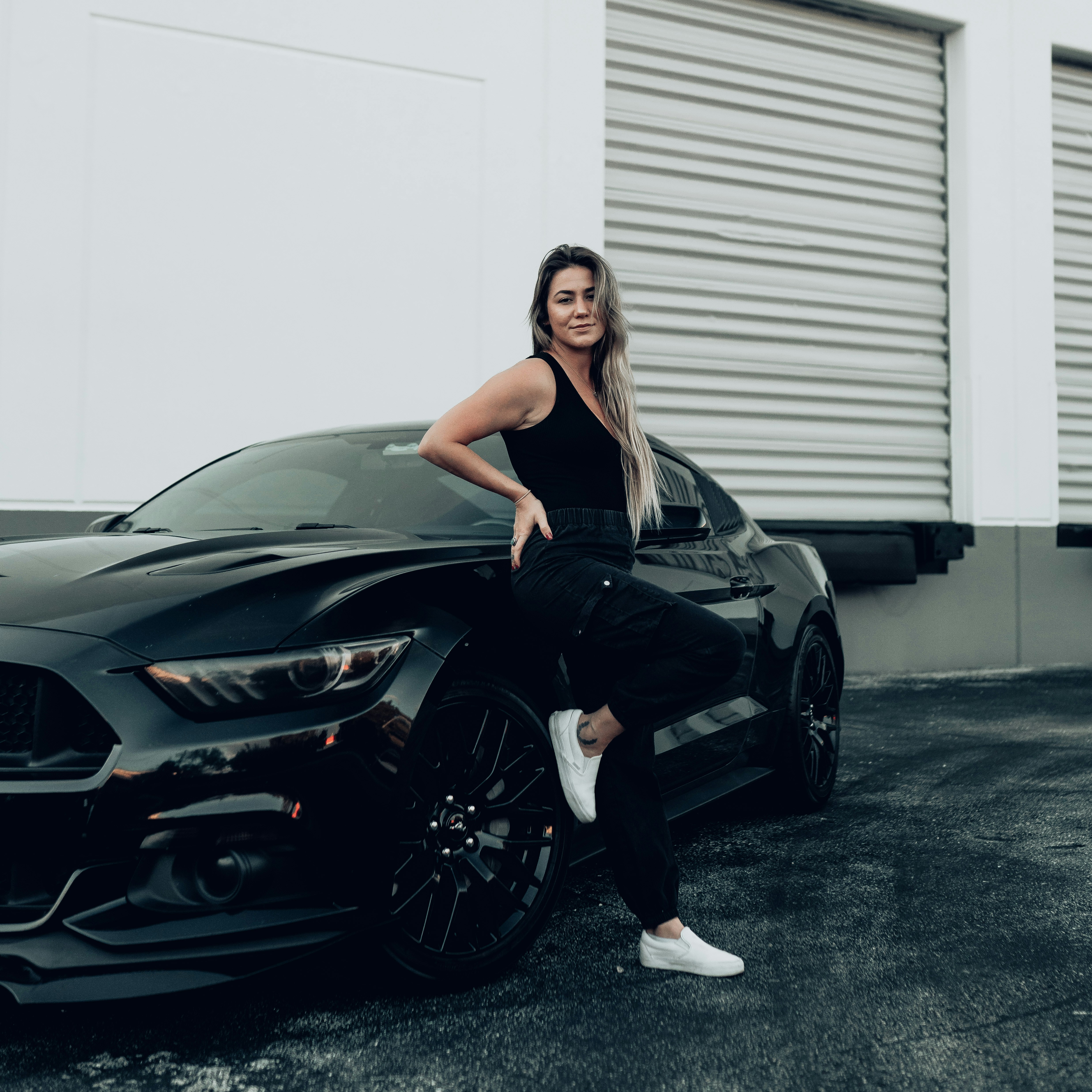 Polished Resolve: A Woman and Her Black Mustang at the Warehouse Edge