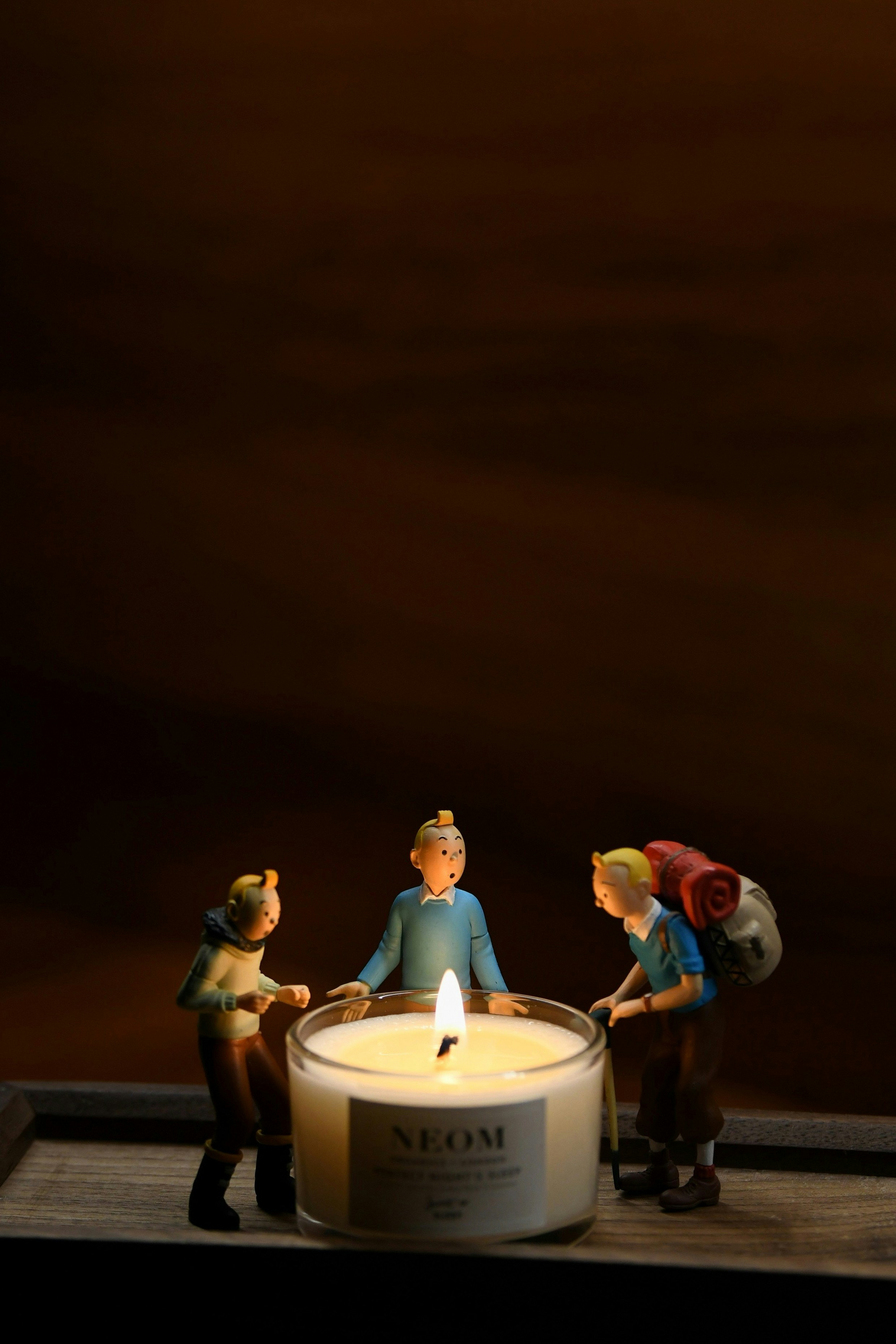 Three figurines huddled around a flickering candle, sharing a moment of intrigue and warmth. The soft glow illuminates their expressions against a dark backdrop.