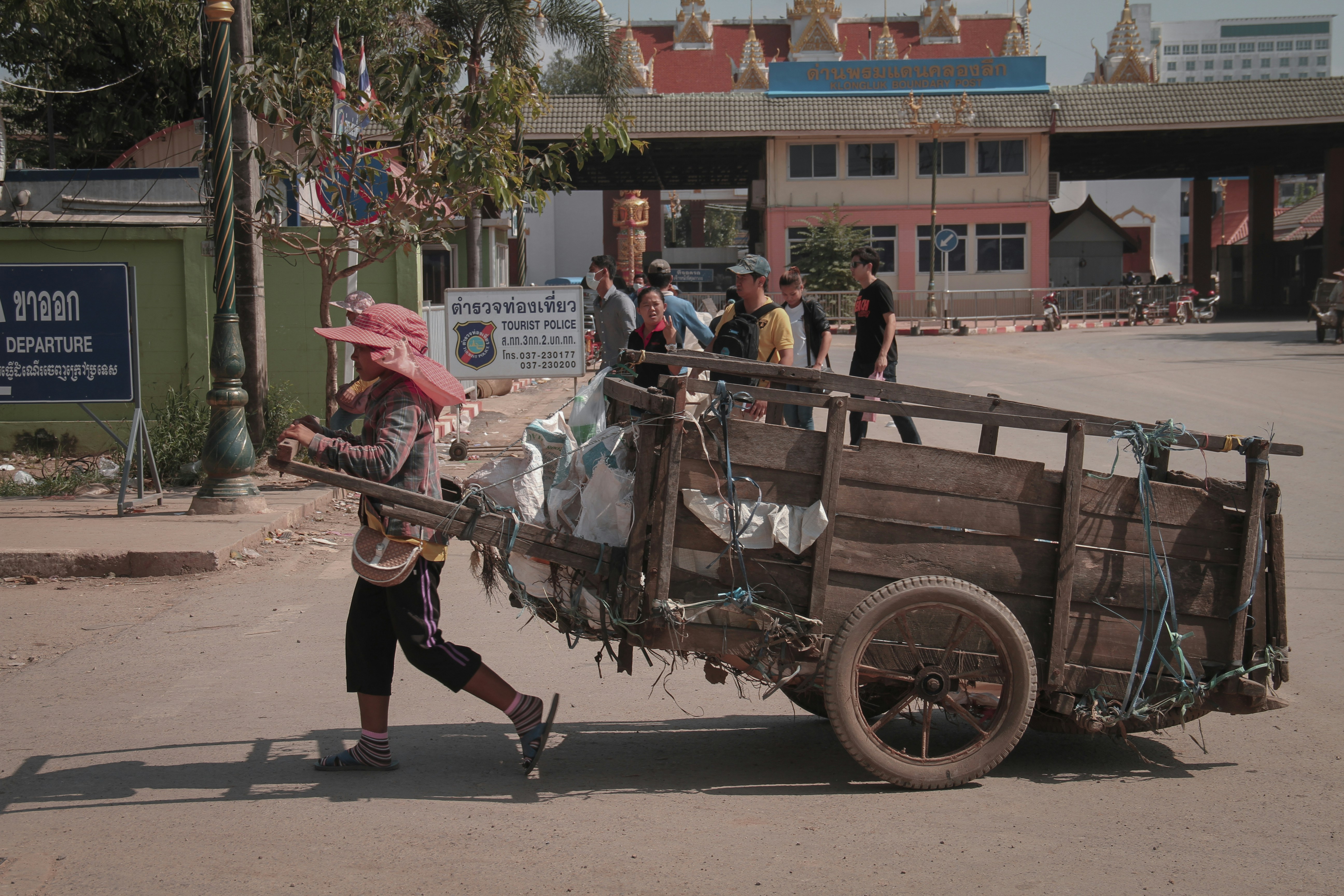 A person in traditional attire pulls a wooden cart laden with items through a bustling street, showcasing the blend of culture and daily life.