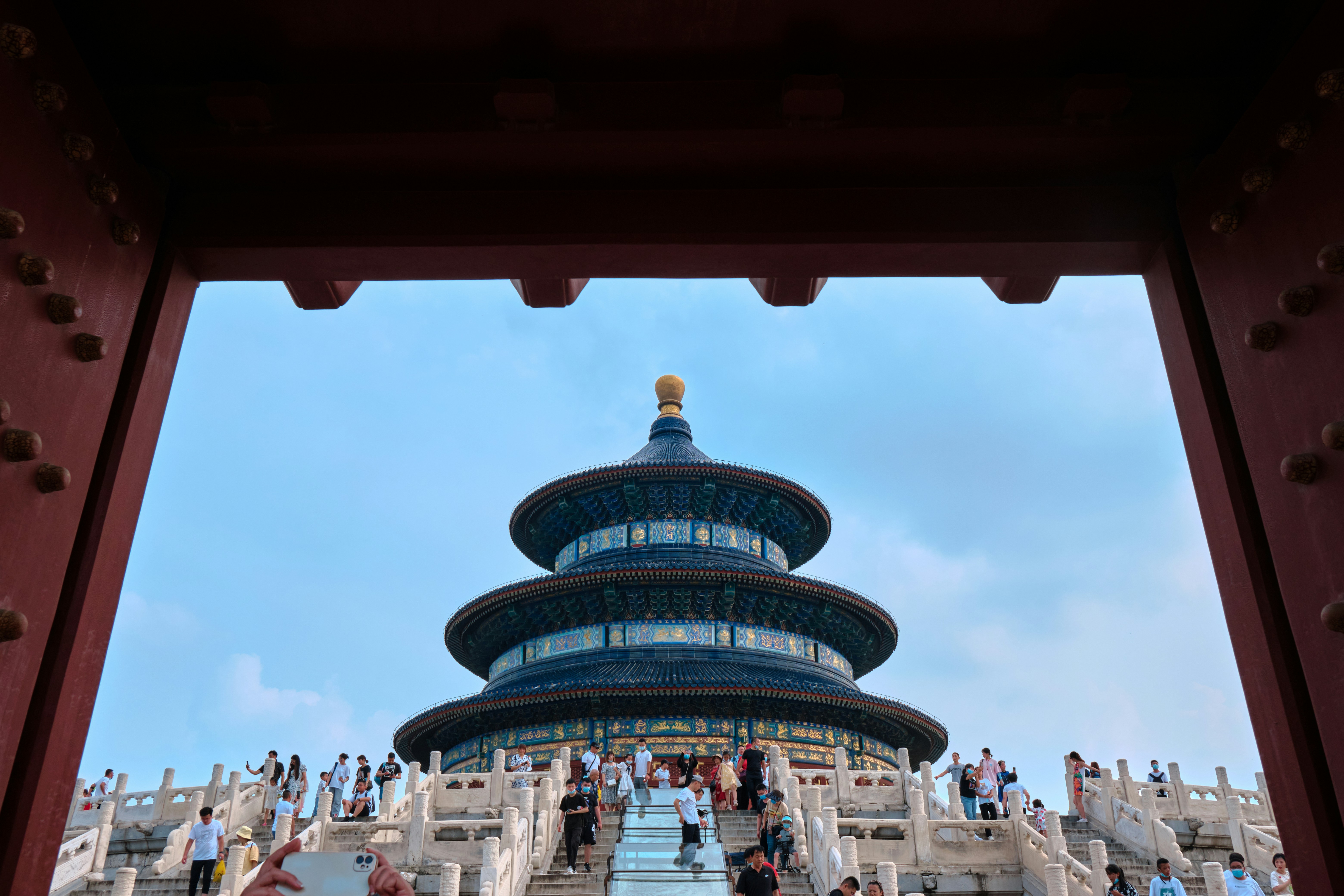 View of the Temple of Heaven framed by an ornate arch, showcasing the intricate architecture and bustling visitors. 