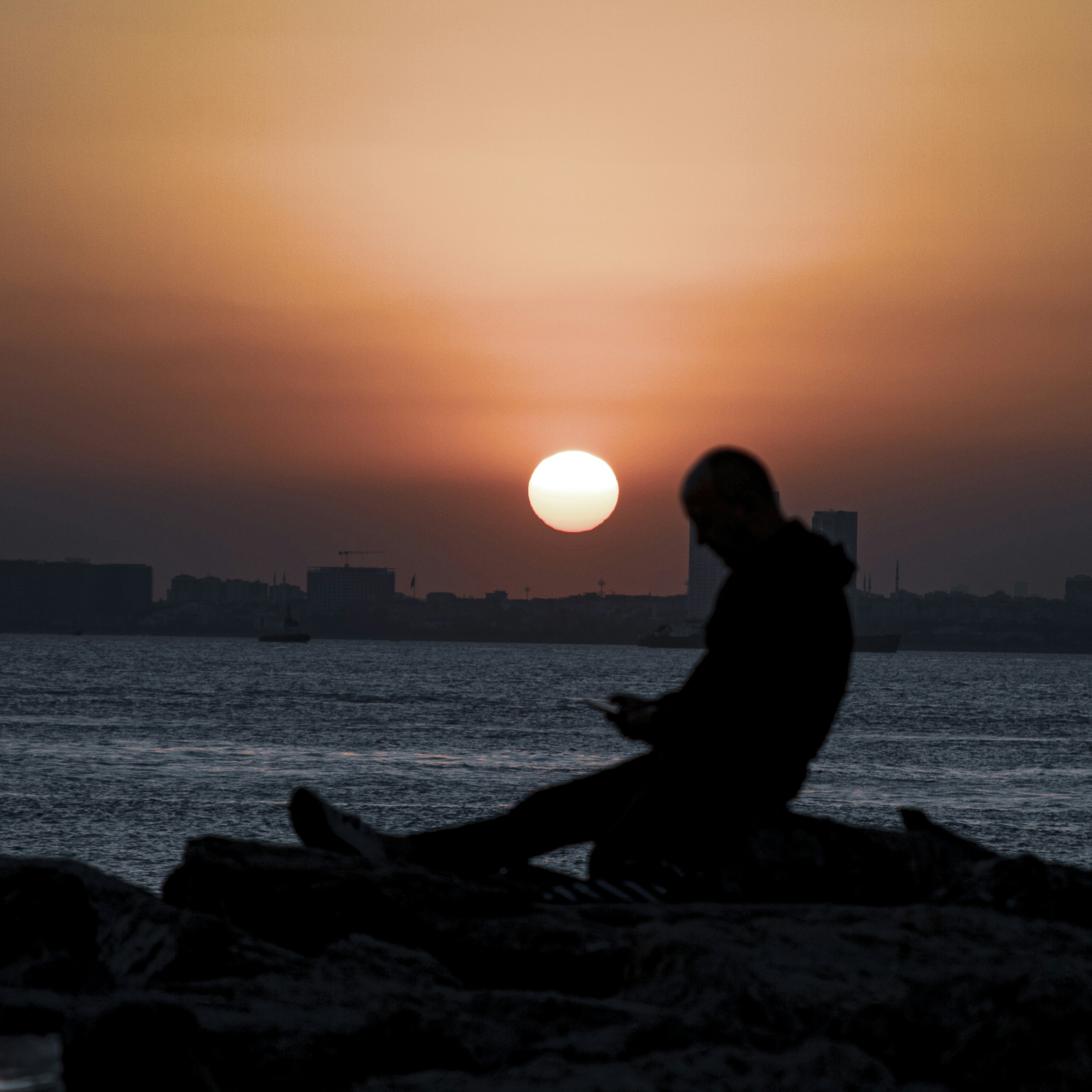 A man sitting on a rock watching the sun set photo – Free Sunset Image ...