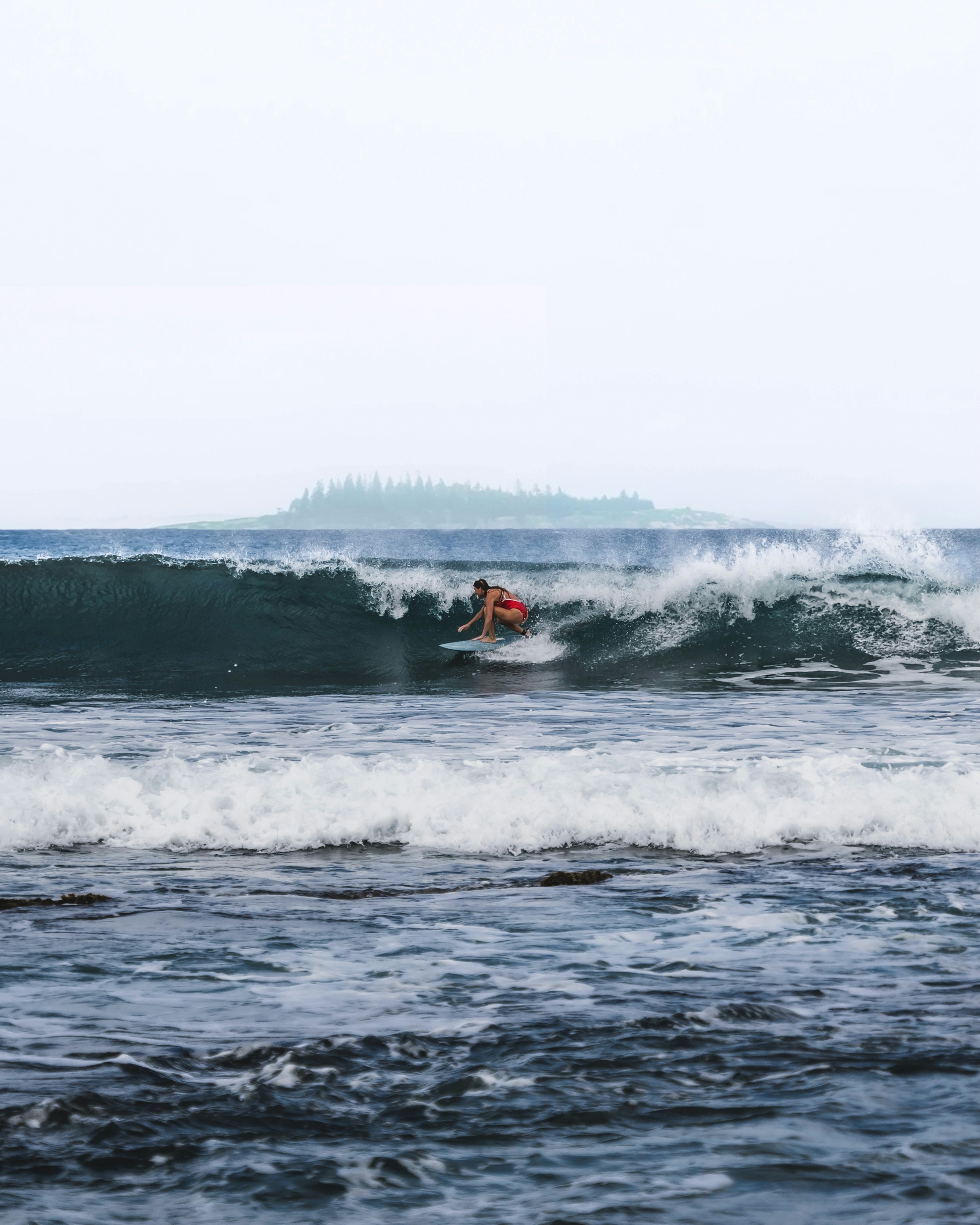 Surfer navigating a wave with a distant island backdrop, showcasing the thrill of ocean sports.