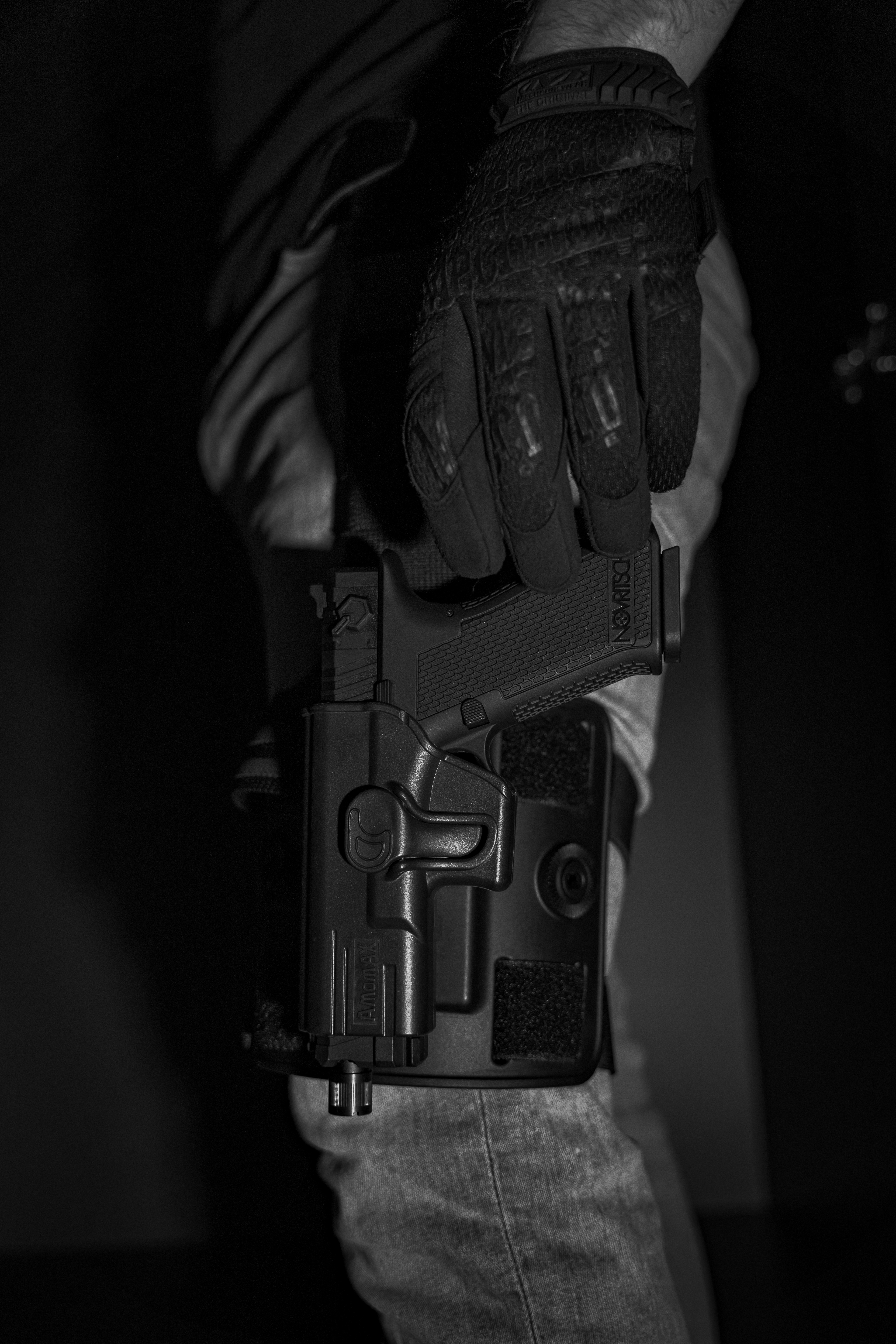 A gloved hand rests on a holstered firearm, emphasizing themes of vigilance and preparedness. The monochromatic tones enhance the dramatic effect.