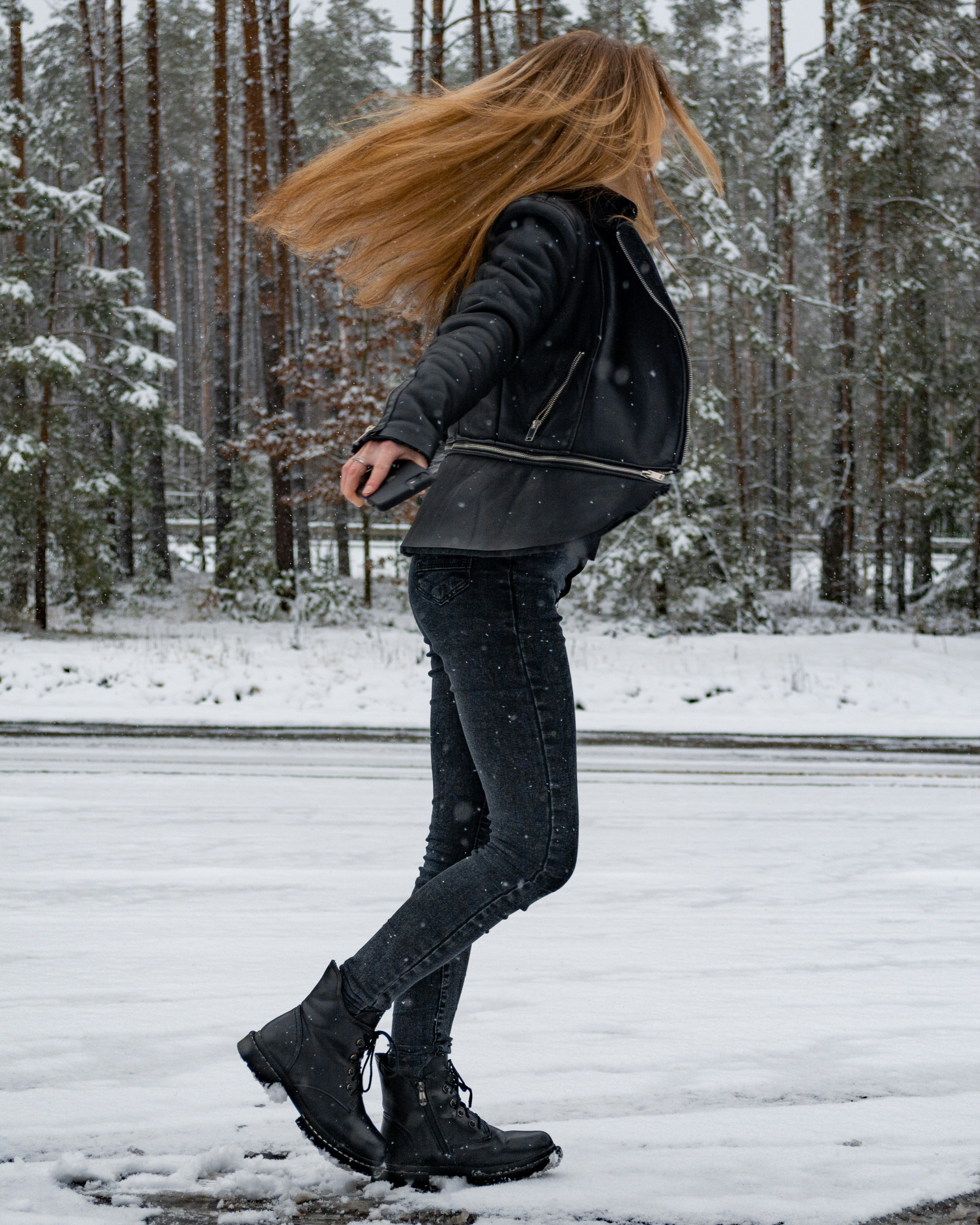 Young woman twirling in the snow, showcasing her flowing hair and stylish winter attire against a snowy forest backdrop.