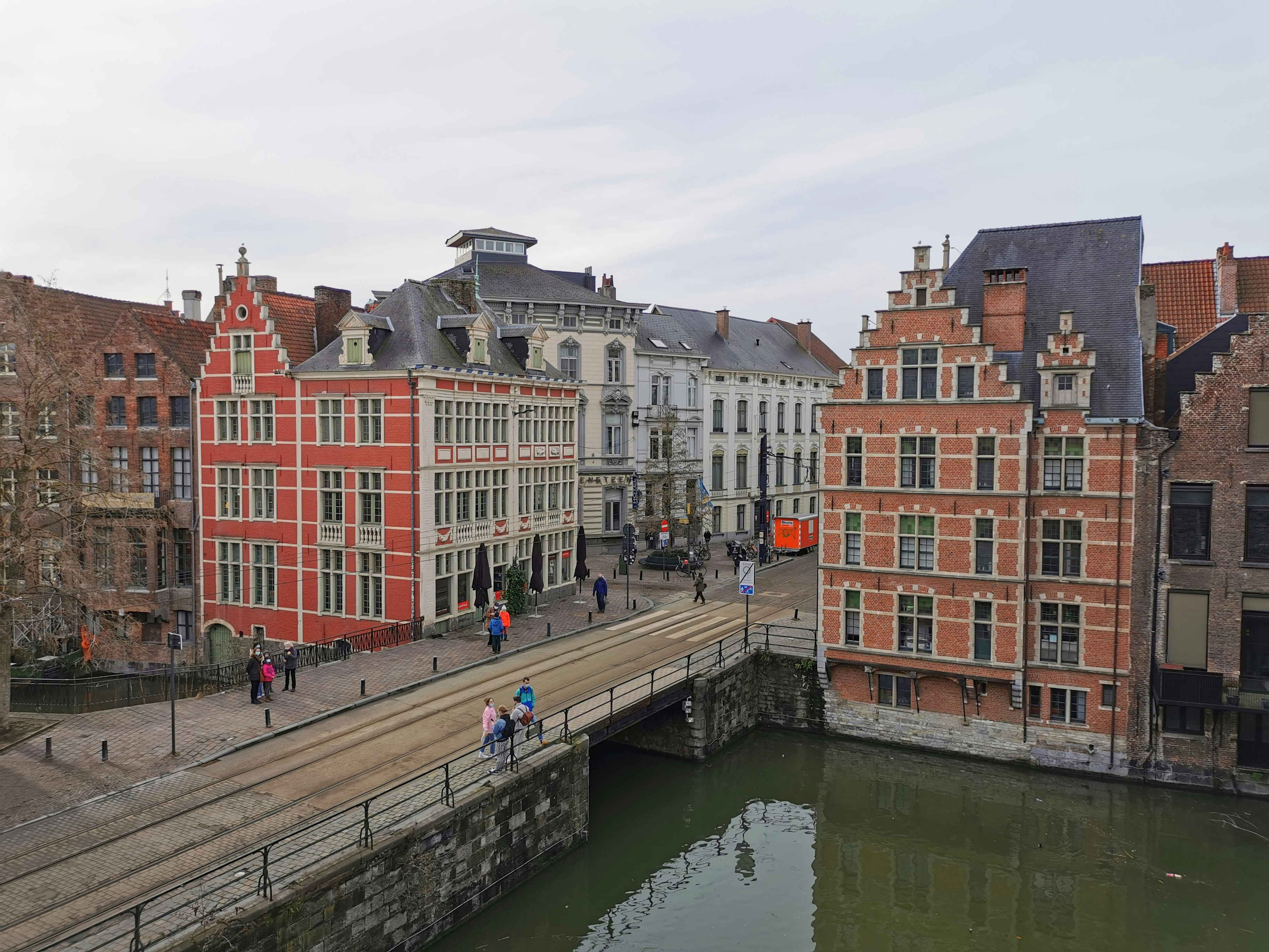Historic European buildings with colorful facades line a canal bridge under a cloudy sky.
