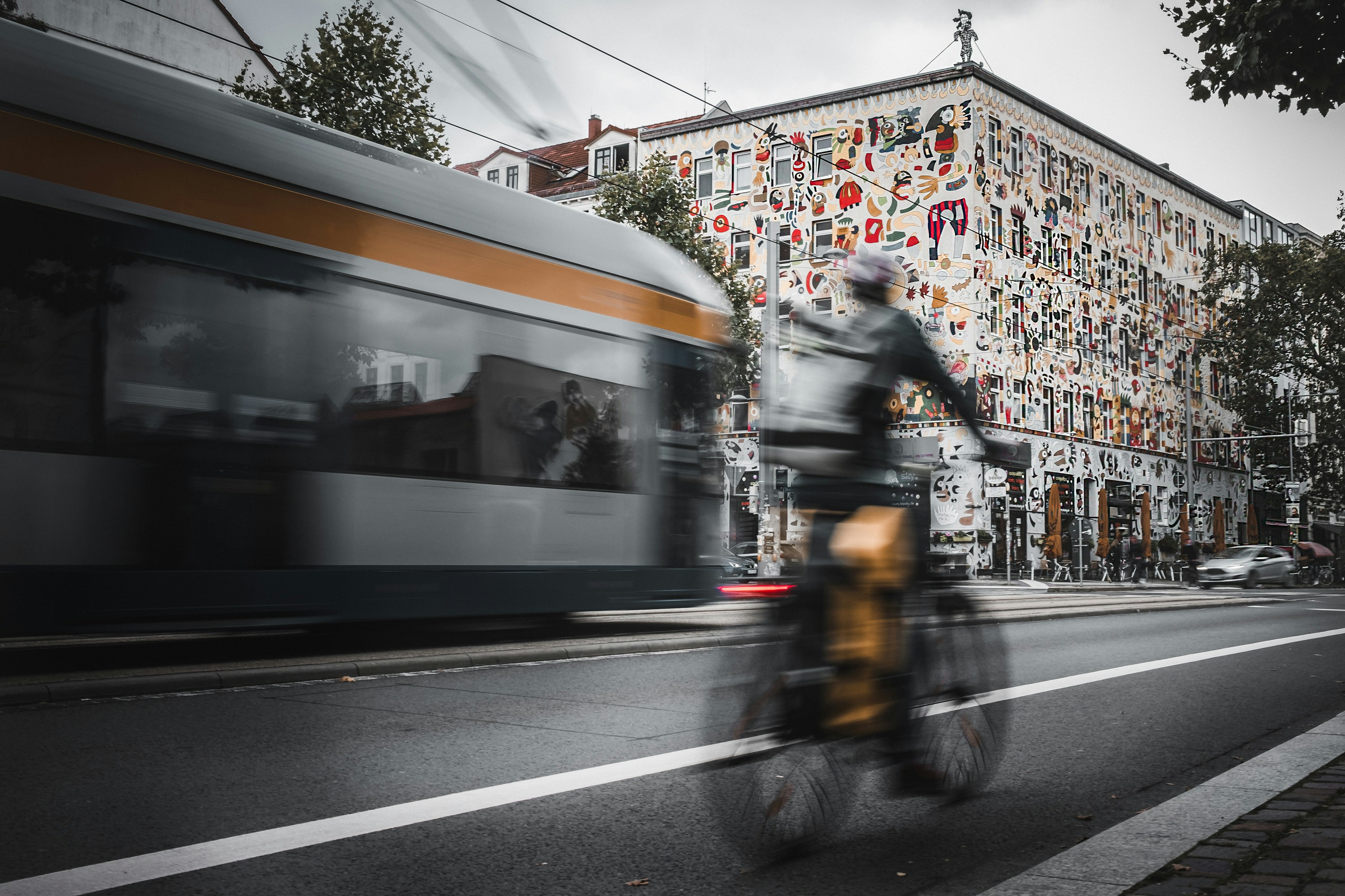 Blurred cyclist and tram against a colorful mural on a city building.