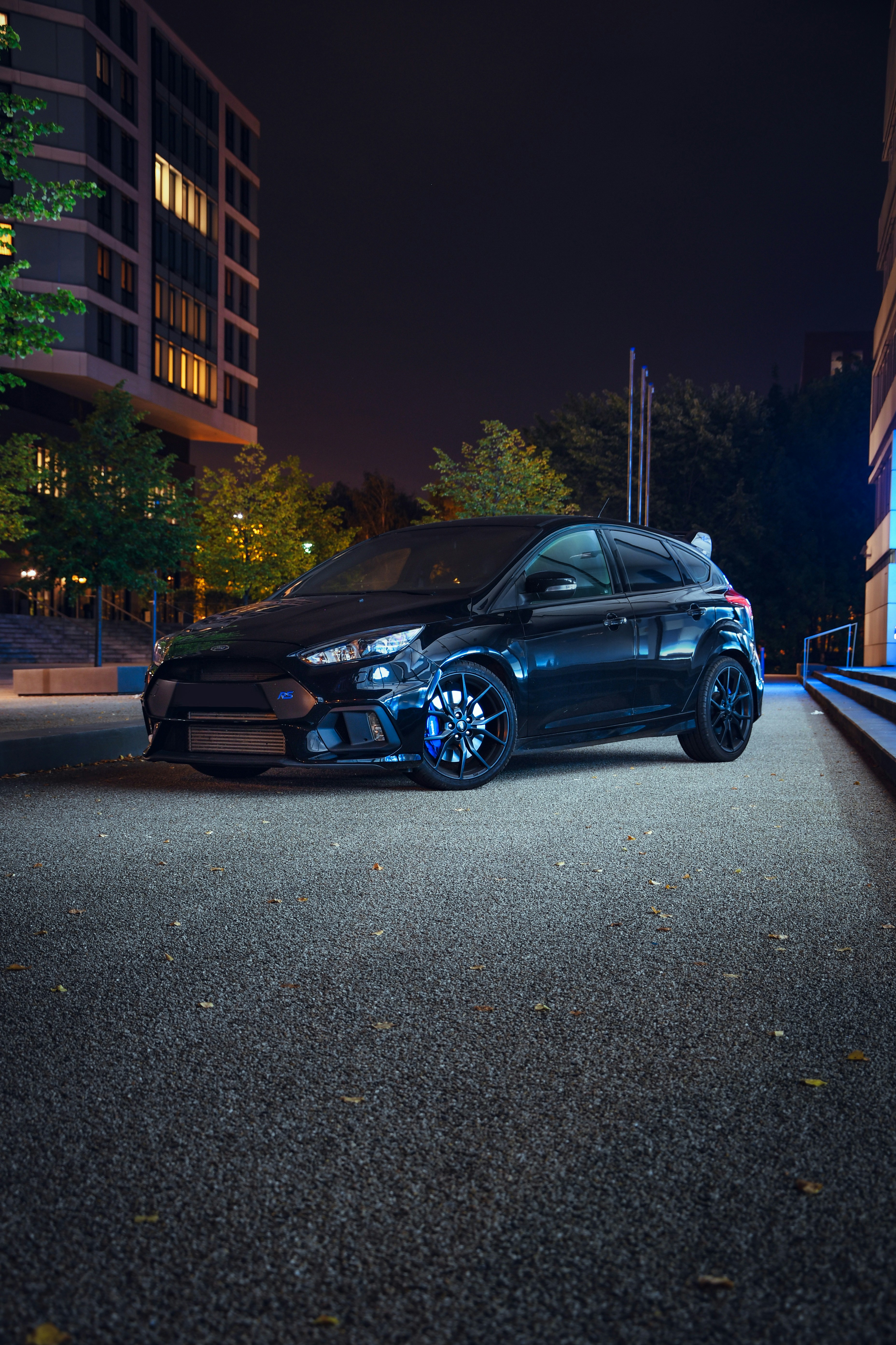 Sleek black sports car parked on a textured surface under urban night lighting, highlighting its aggressive design and modern aesthetics.